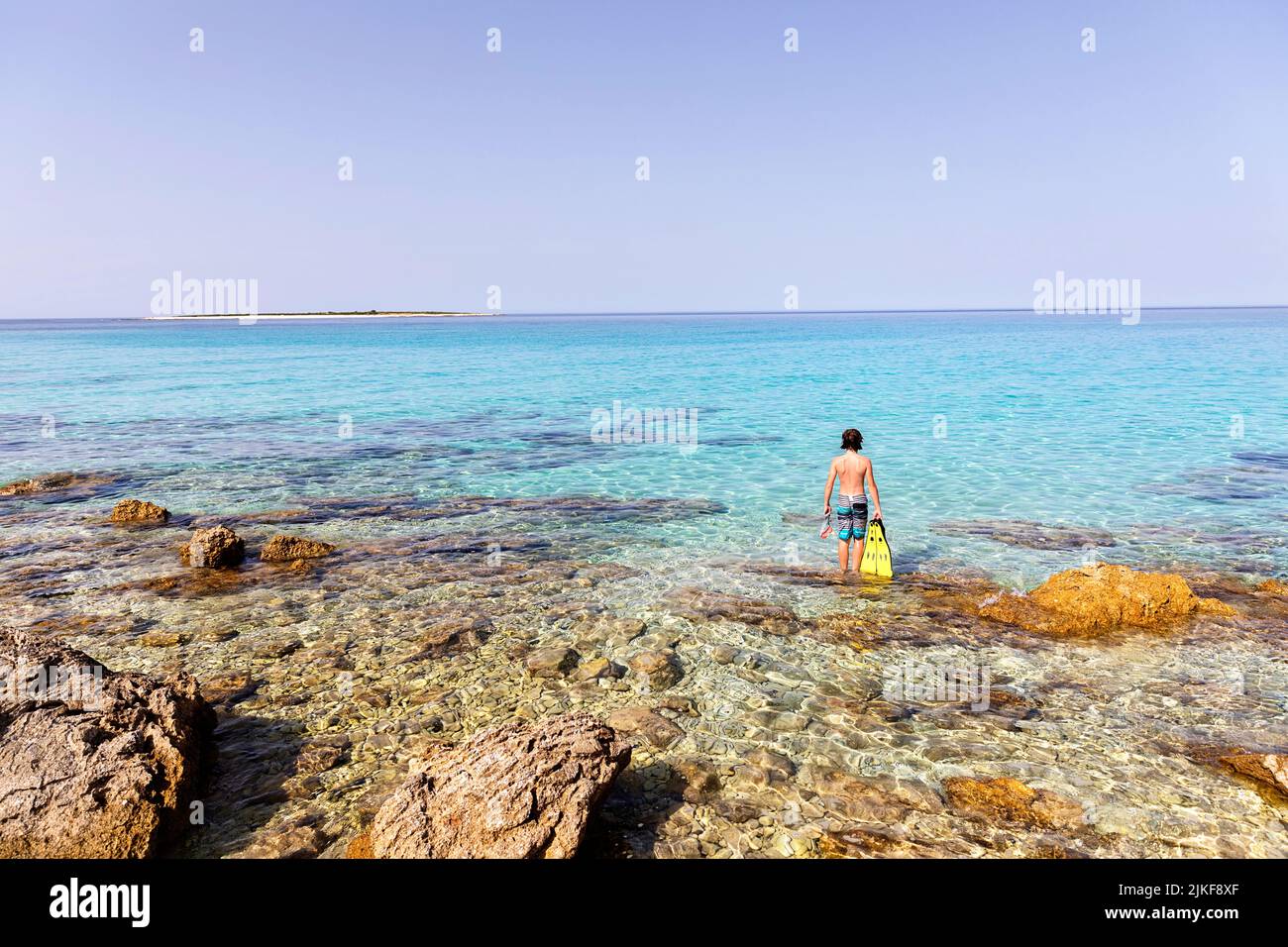 Boy standing on a beach with snorkeling fins in his hands on a ...