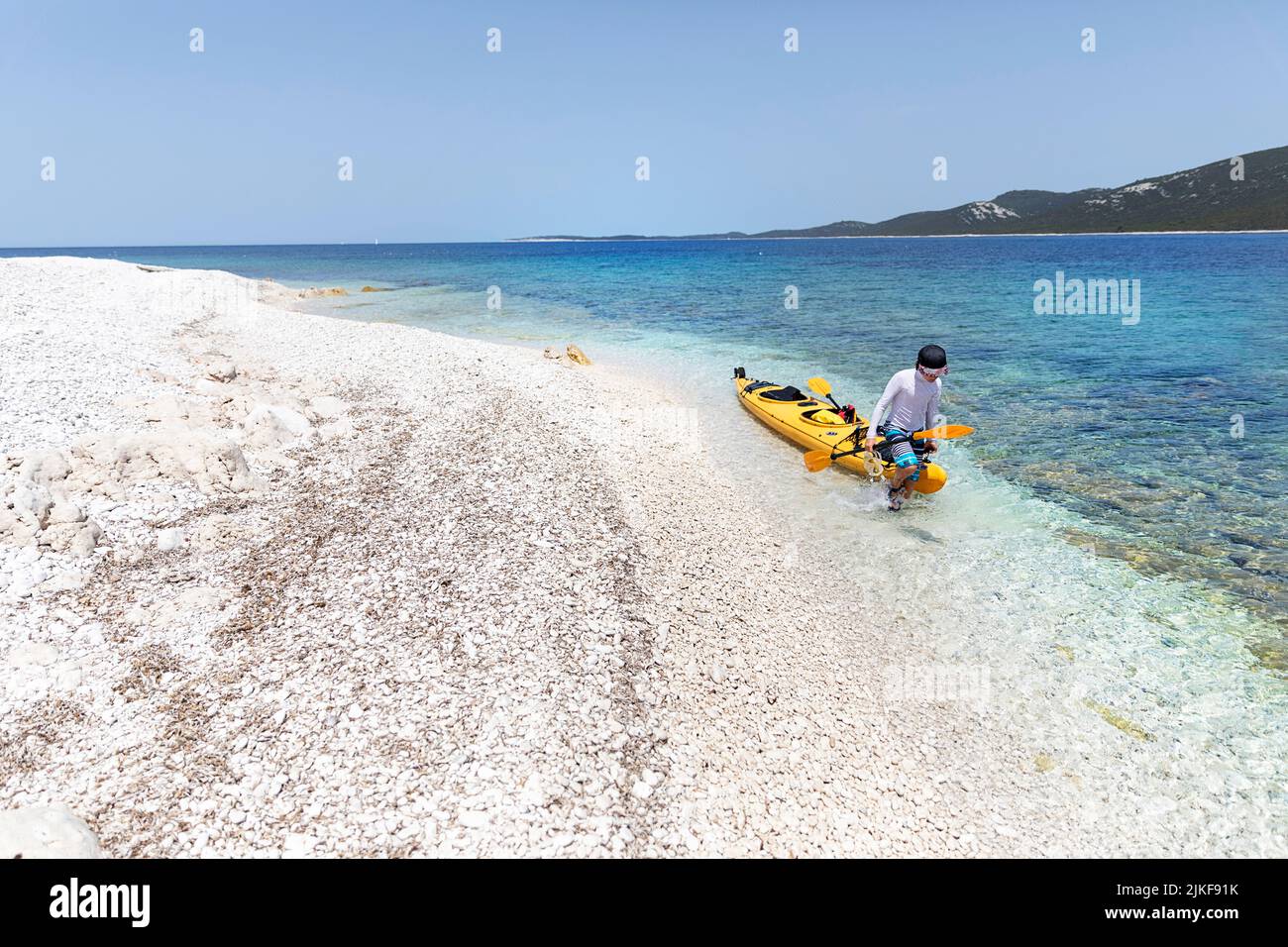 Boy walking in the sea and pulling sea kayak on an uninhabited island ...