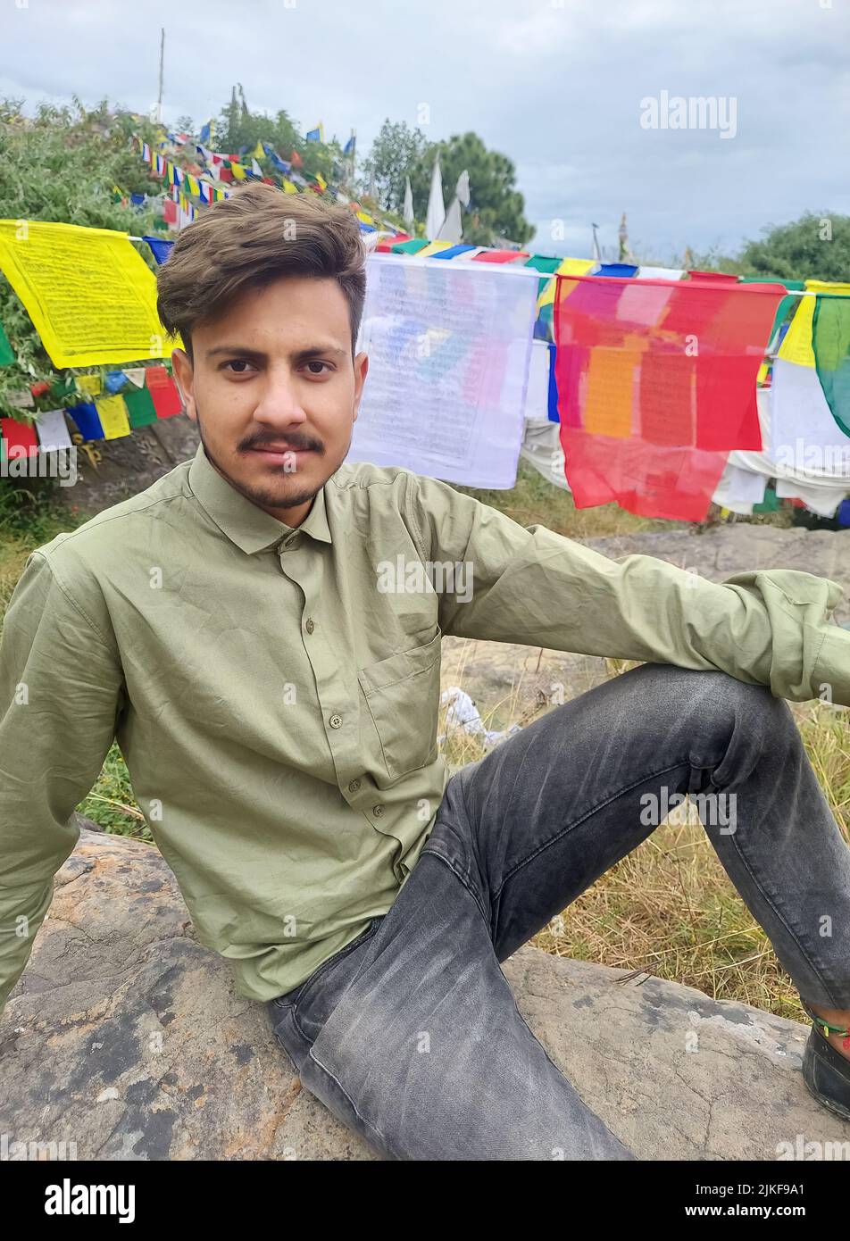A handsome young guy looking at camera while sitting on rock with the ...