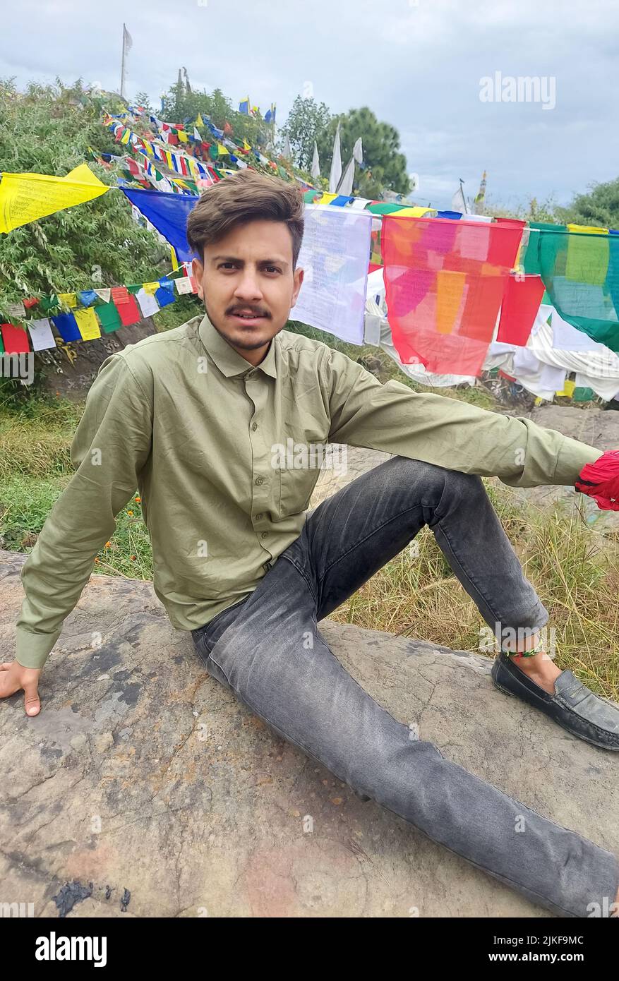 A handsome young guy looking at camera while sitting on rock with the ...