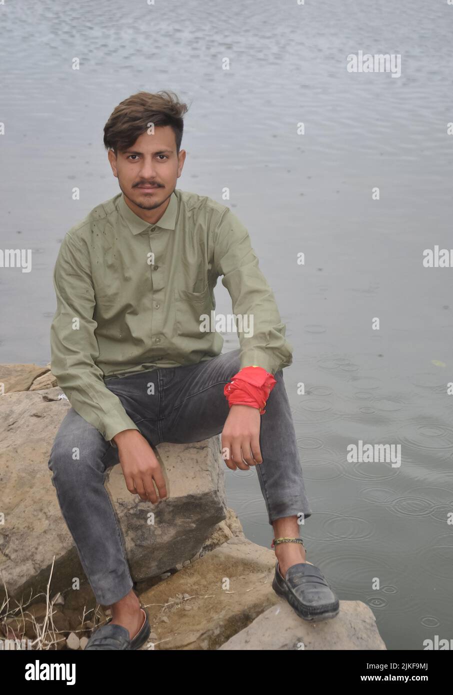 A young guy looking at camera while sitting on stone next to the lake ...
