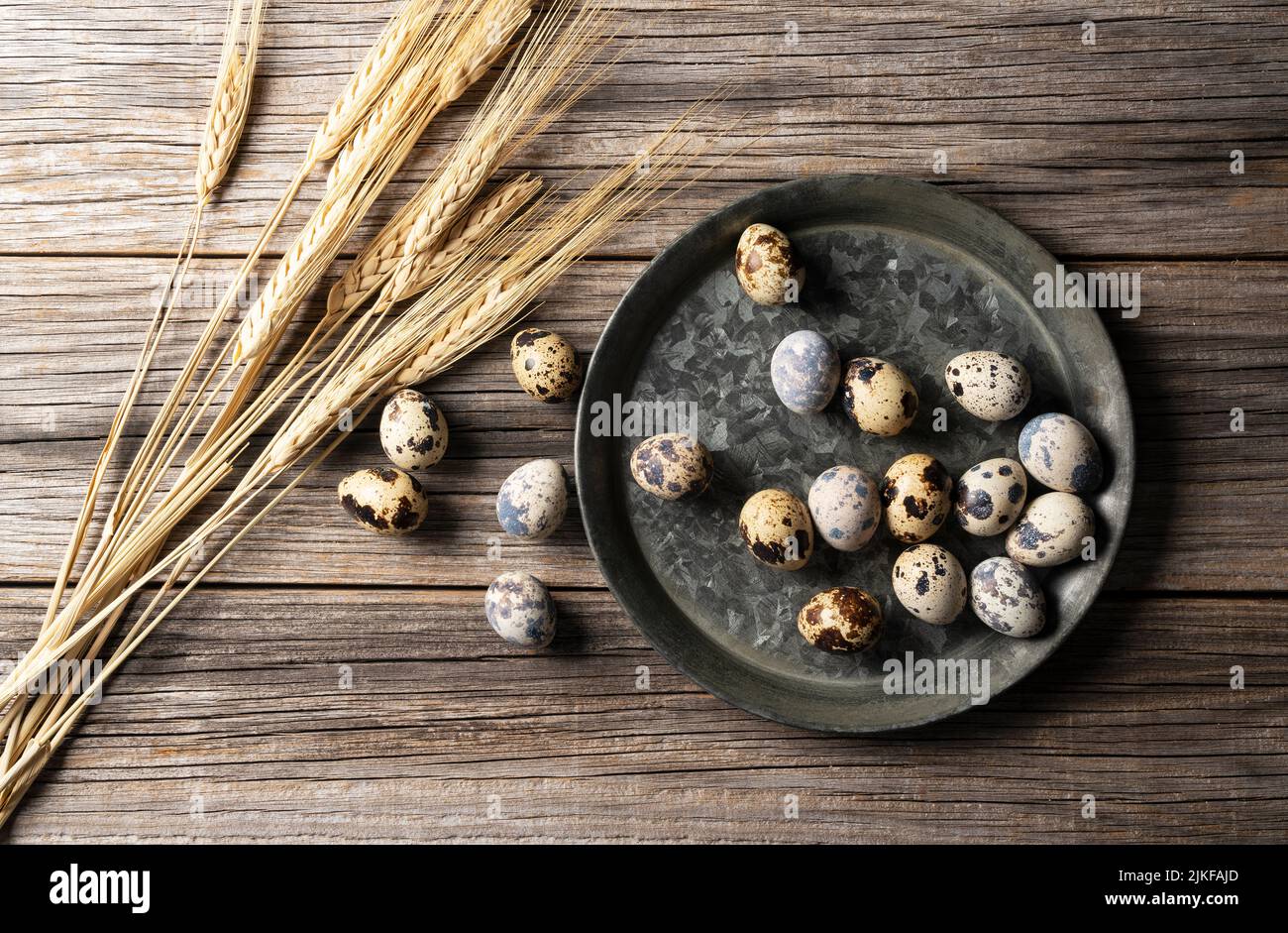 Quail eggs and ears of wheat in an iron dish placed against a wooden ...