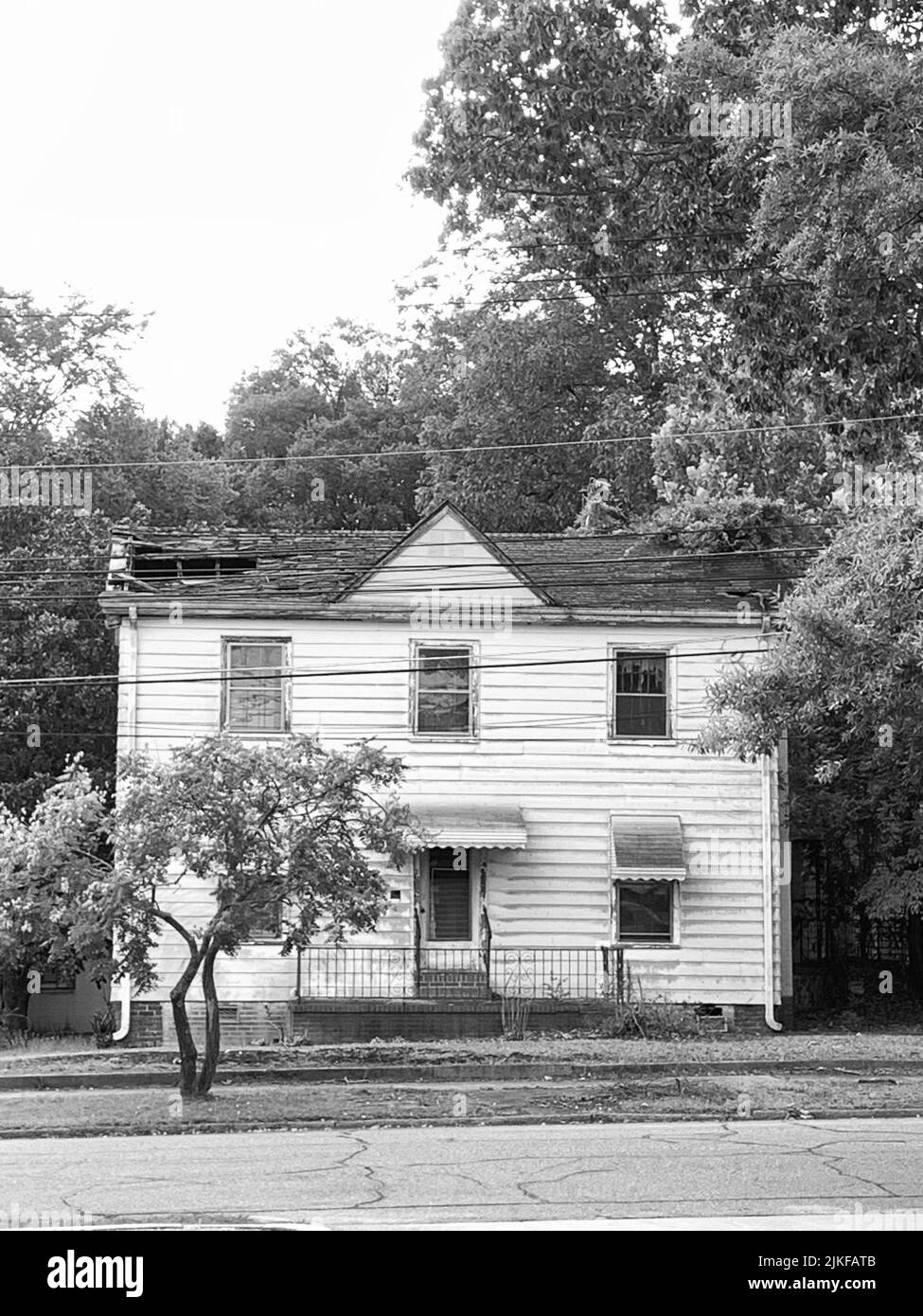 A vertical grayscale shot of old wooden house surrounded by lush trees ...