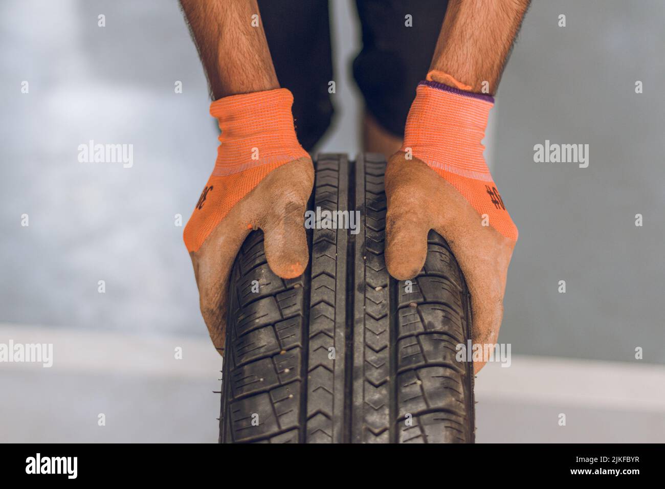 Pakistani or Indian or South Asian car mechanic rolling tire with hands ...