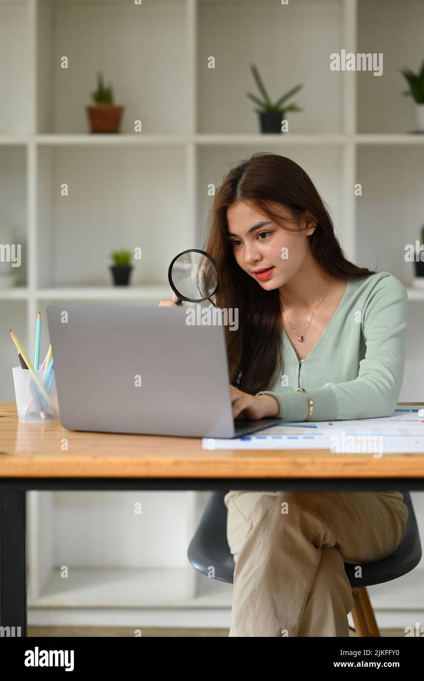 Concentrated female auditor holding magnifying glass examining the ...