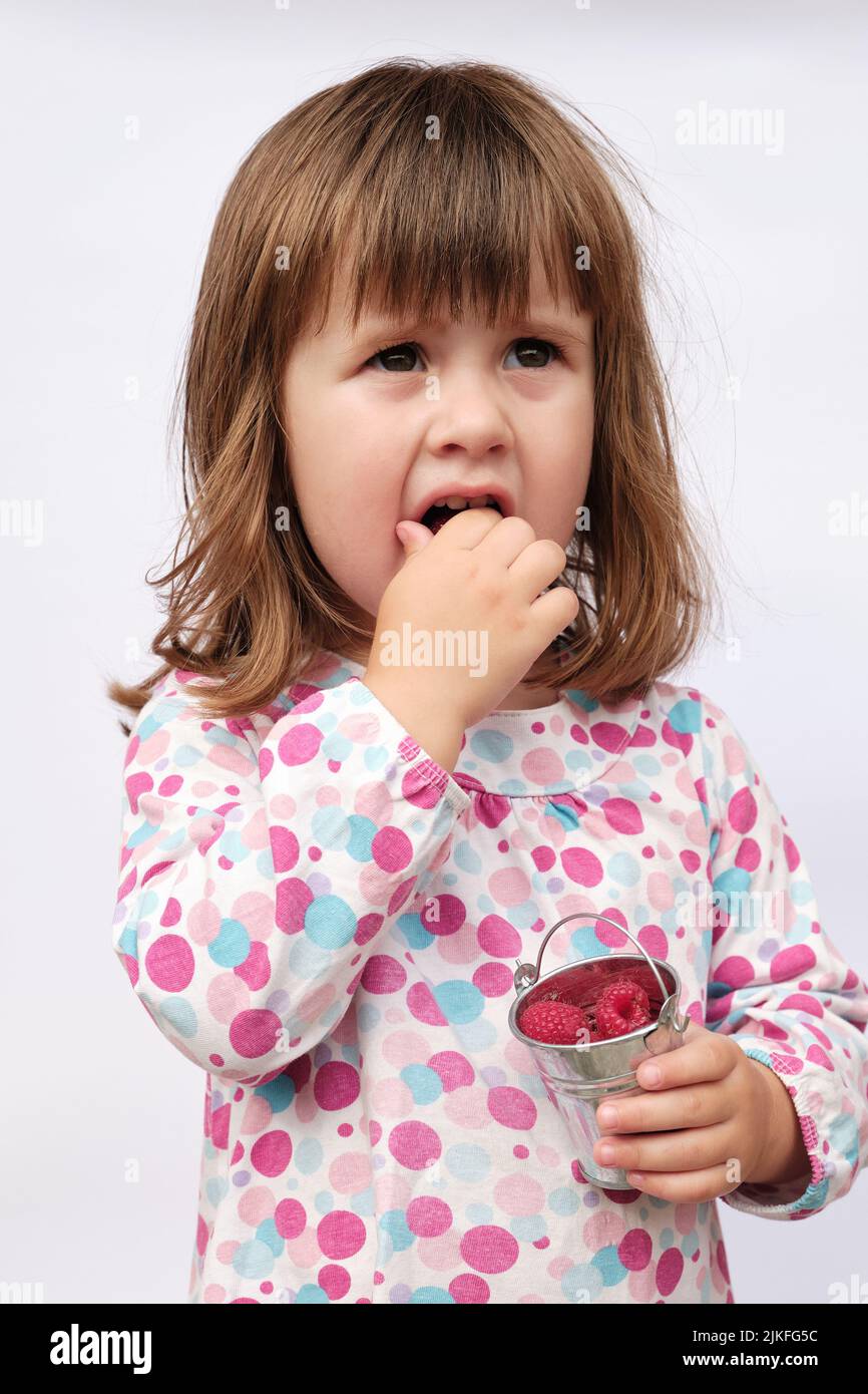 Little baby eating raspberry from decorative metal bucket. Cute little ...