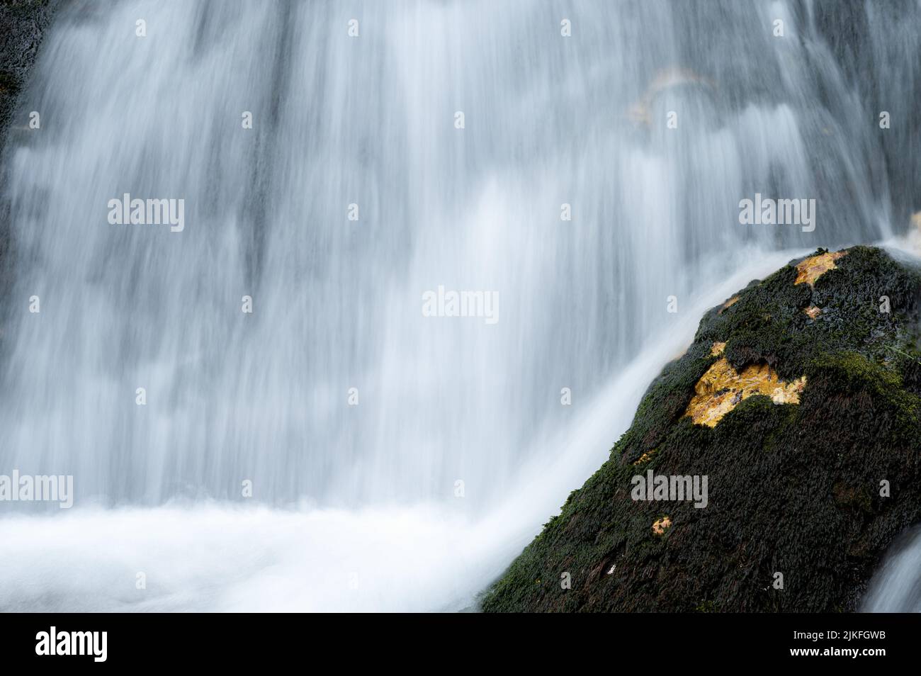 Beautiful wide blurred waterfall falling in the background of a mossy ...