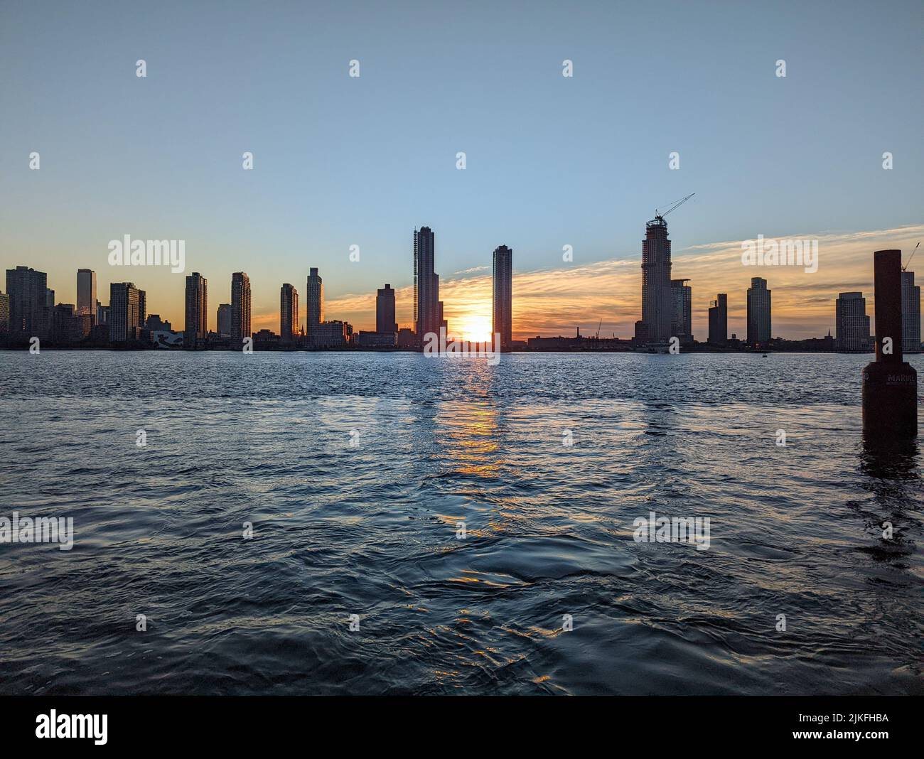 A dramatic sunset behind the skyscrapers of NYC on the shore Stock ...