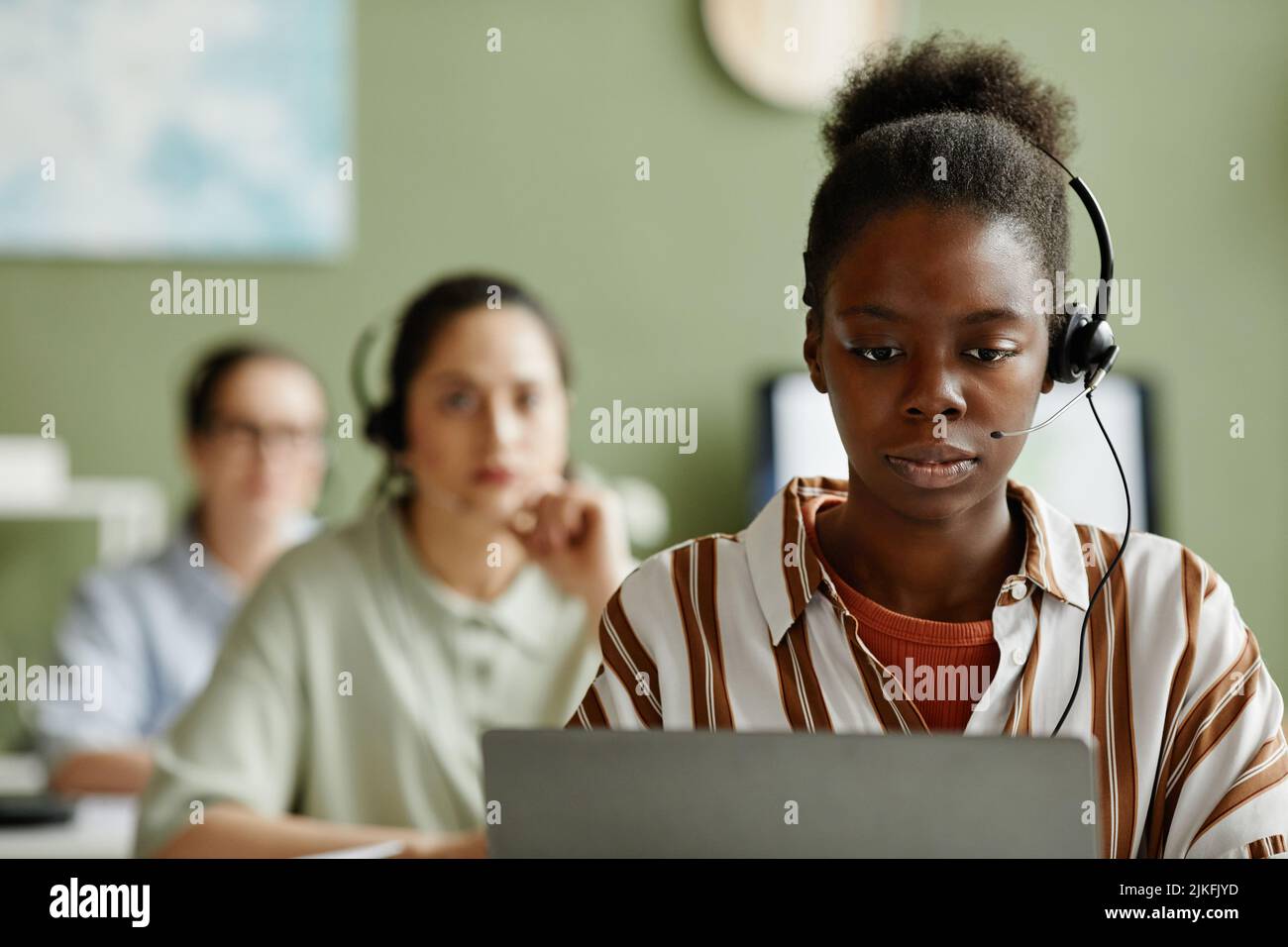 African young agent in headphones sitting in front of laptop working in ...