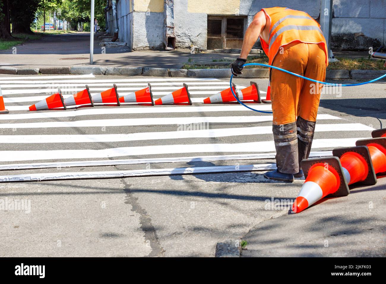 A road worker in orange overalls draws white road markings of a ...
