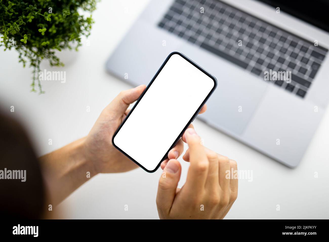 Man using smartphone blank screen frameless modern - top view, laptop keyboard in background ...