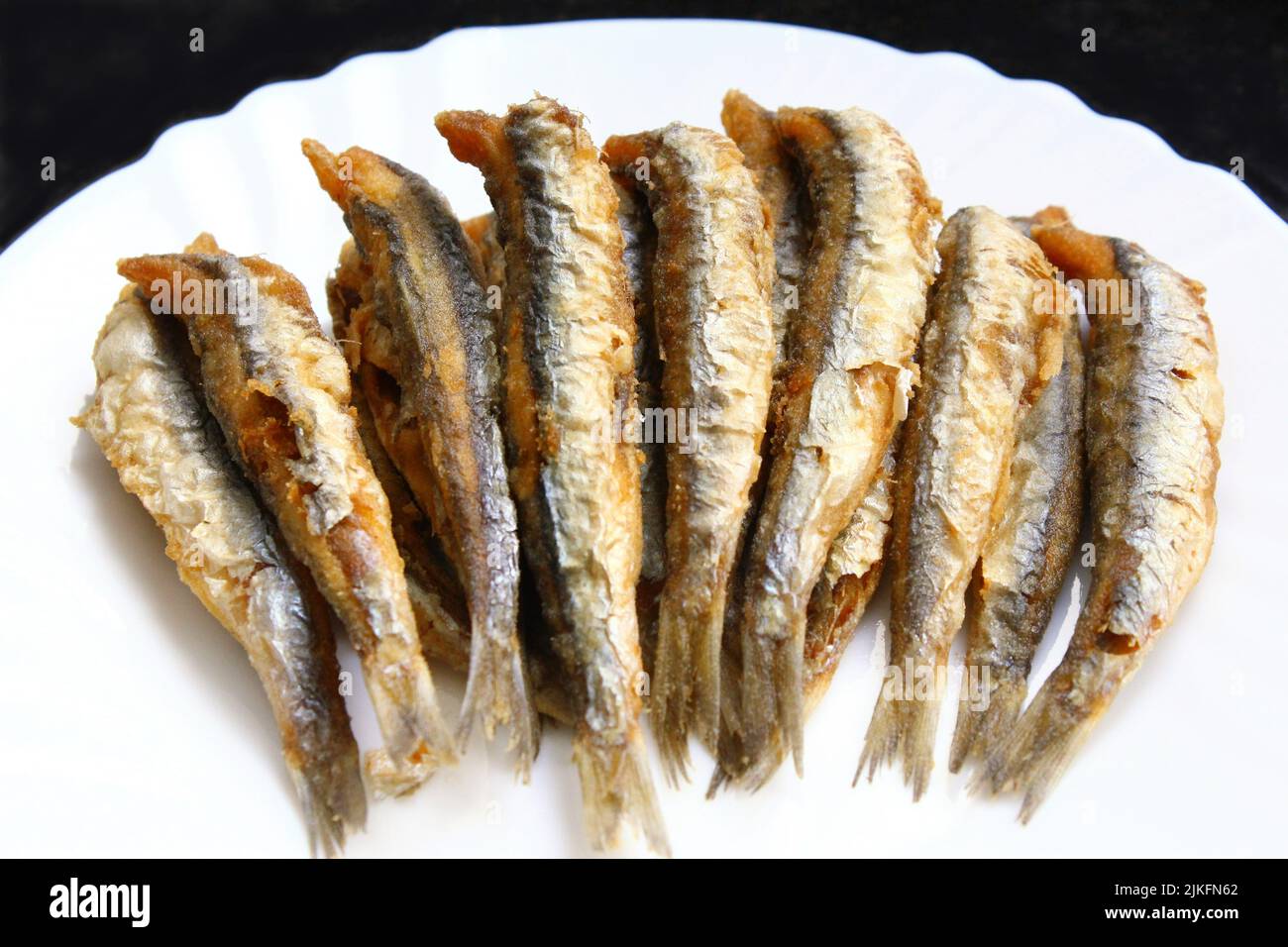 Fried anchovy fish on white plate. close up photo isolate on black top ...