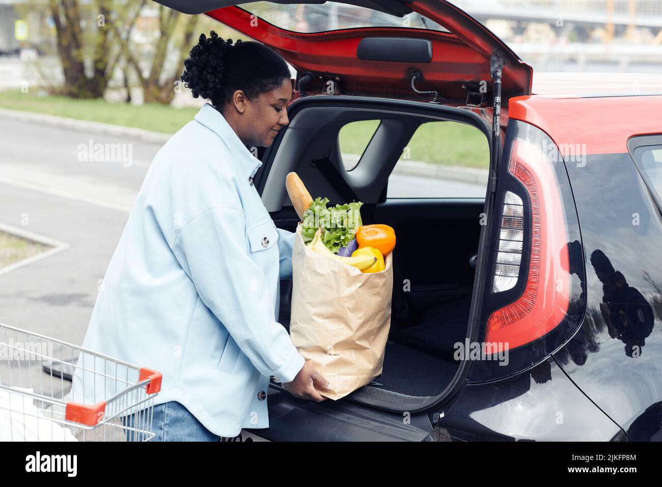 Side view portrait of smiling black woman putting groceries in car ...