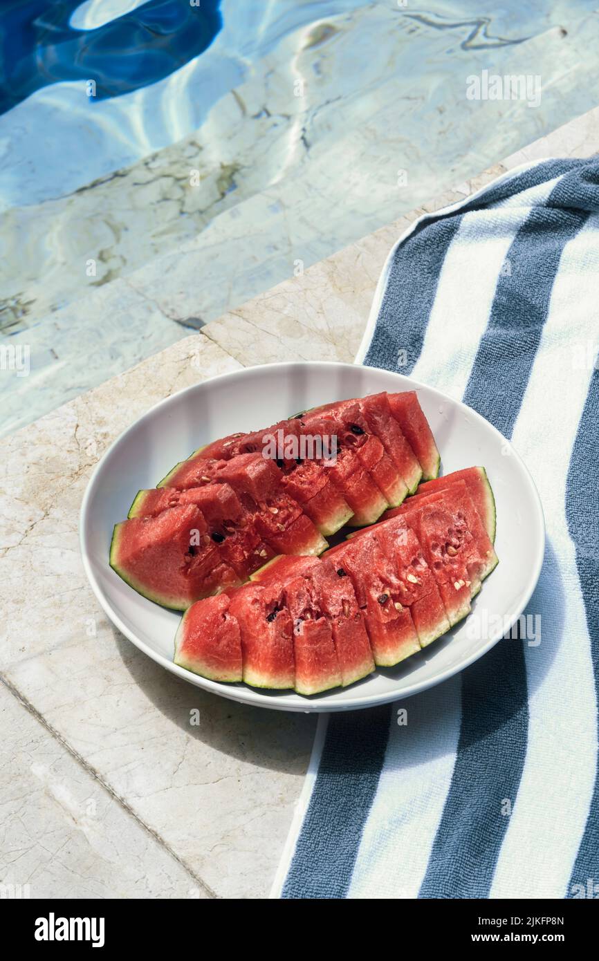 Sliced watermelon in a white plate in front of the pool. View from ...
