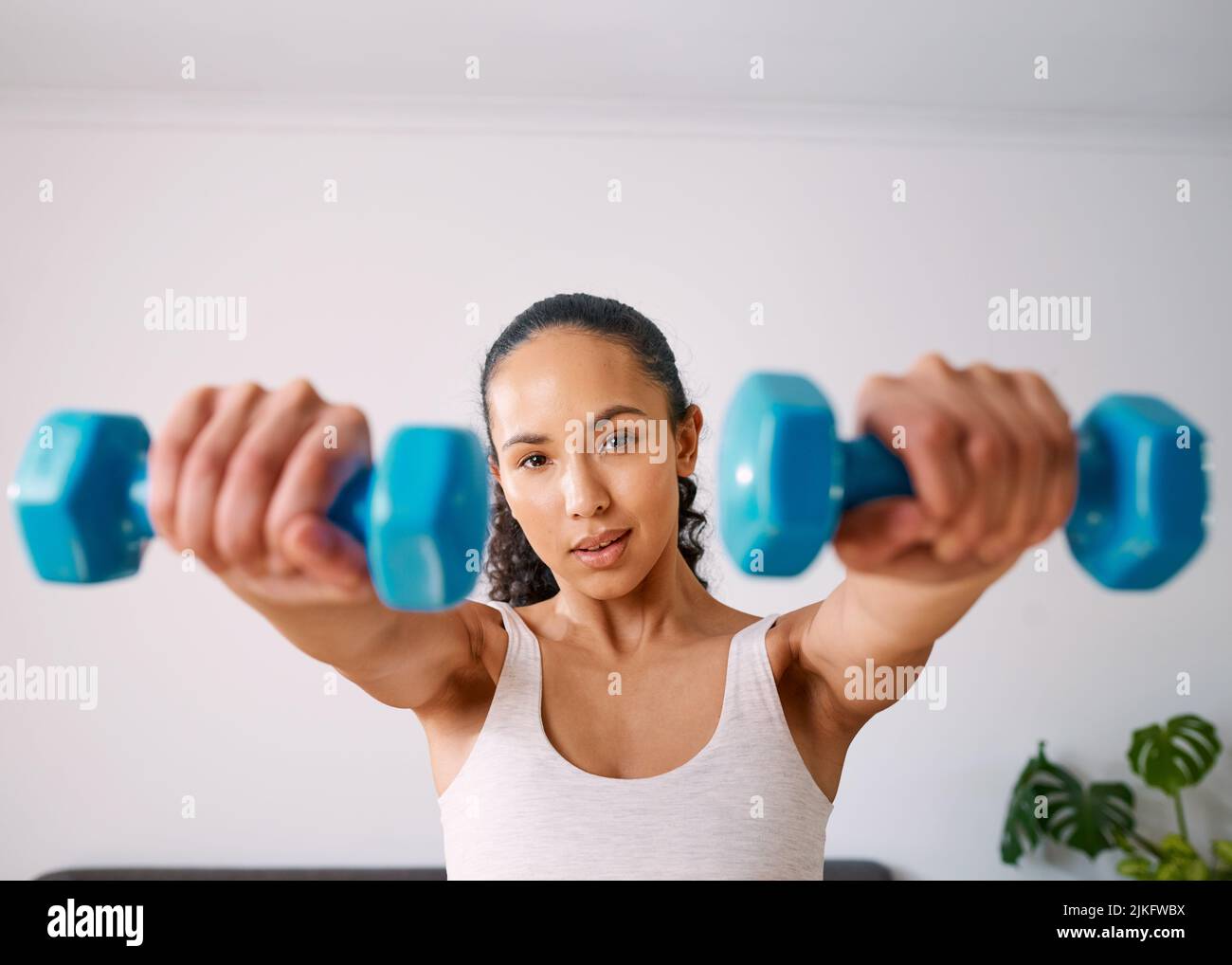 A serious young woman lifts small weights to get strong at home Stock ...