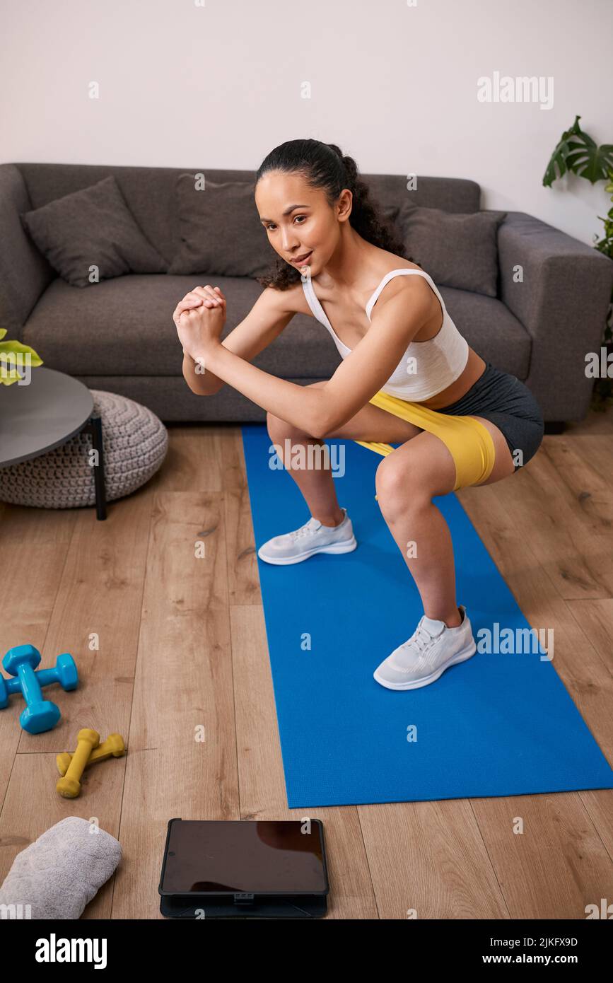 A young woman squats with resistance band during home work out Stock ...