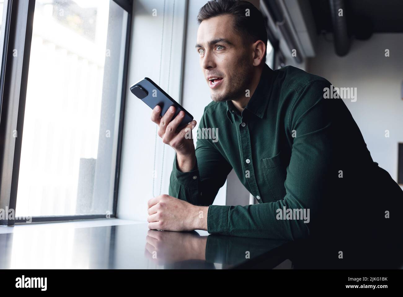 Caucasian young businessman talking on smart phone speaker by window at ...
