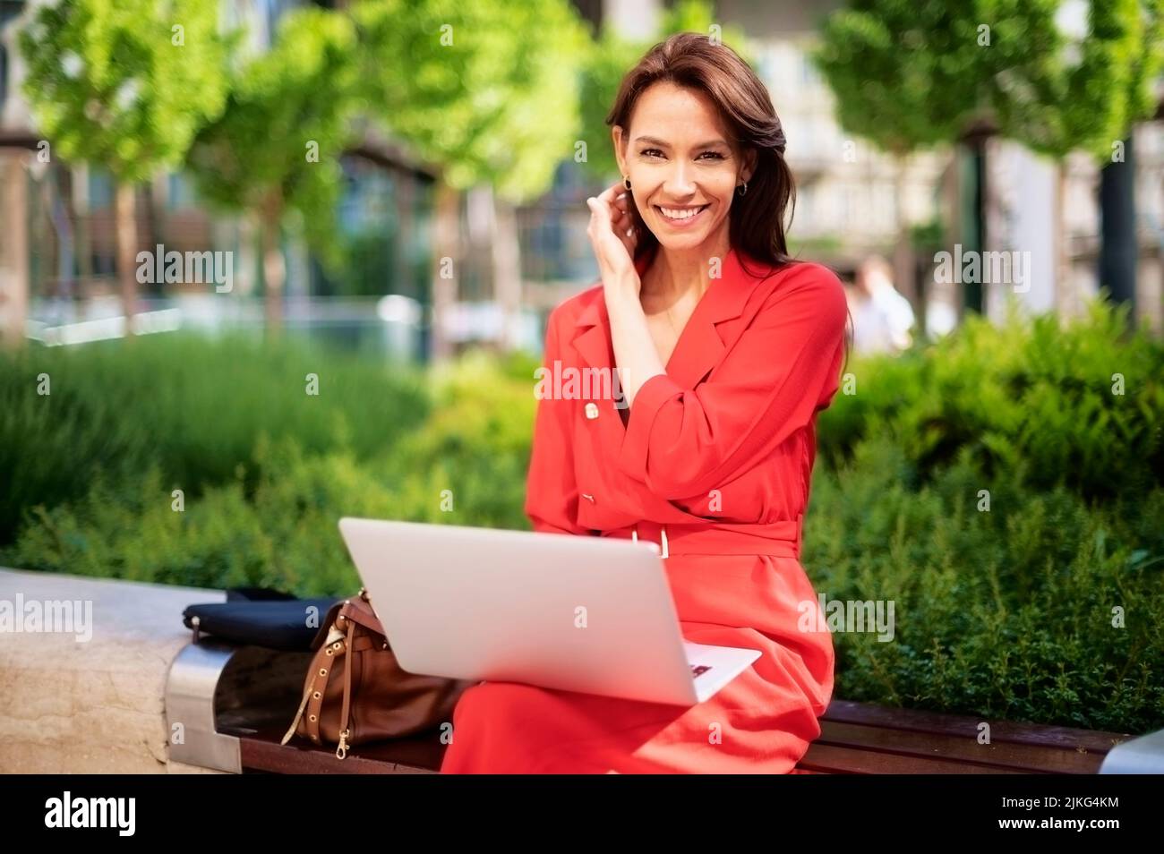 Attractive businesswoman using her laptop while sitting on the bench at ...