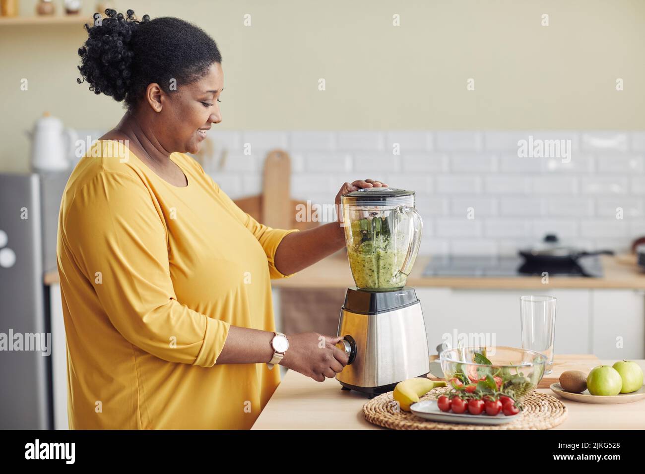 Side view portrait of young black woman using blender while making ...