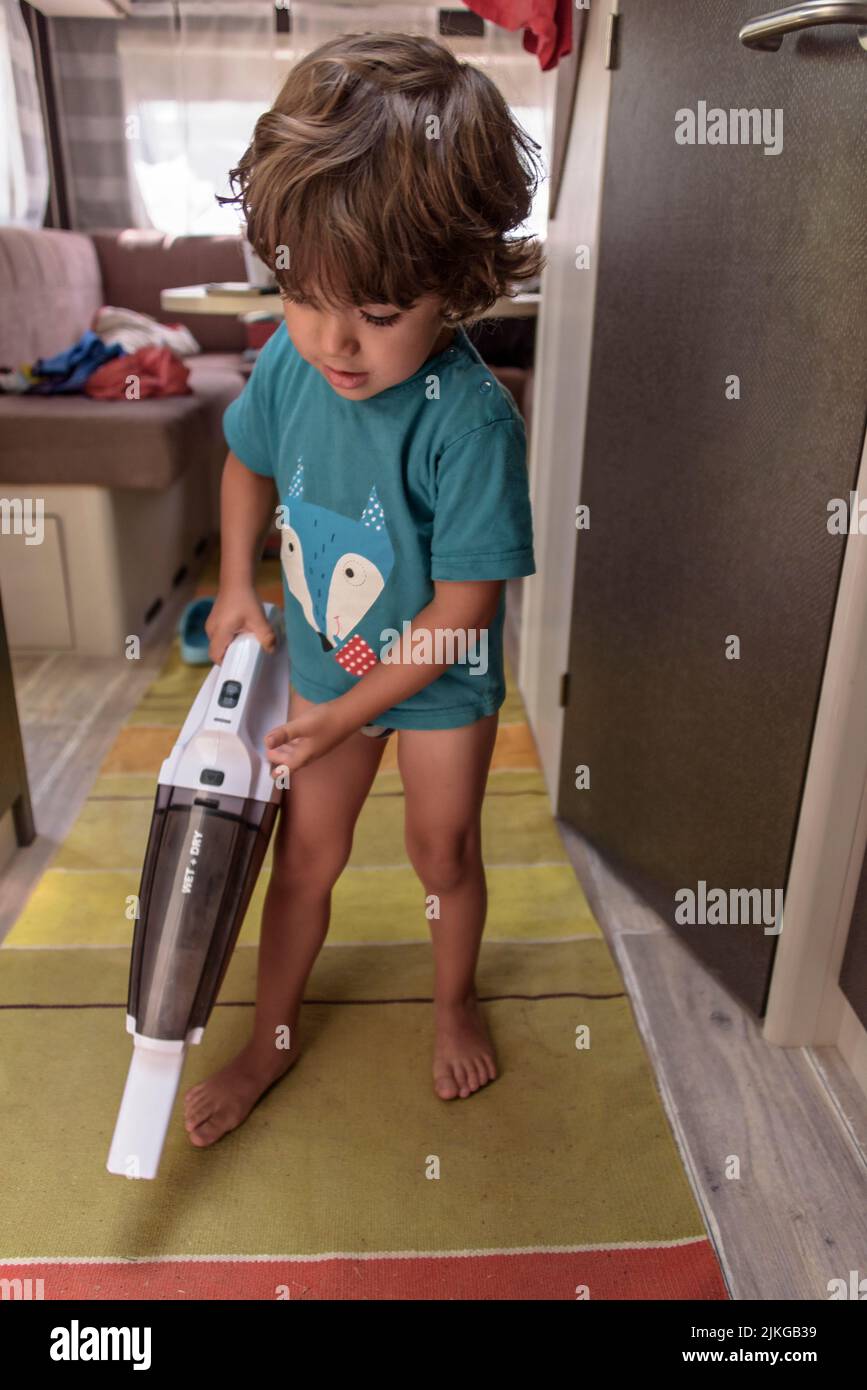 A sweet little boy vacuums the caravan while on vacation. A cute boy is ...