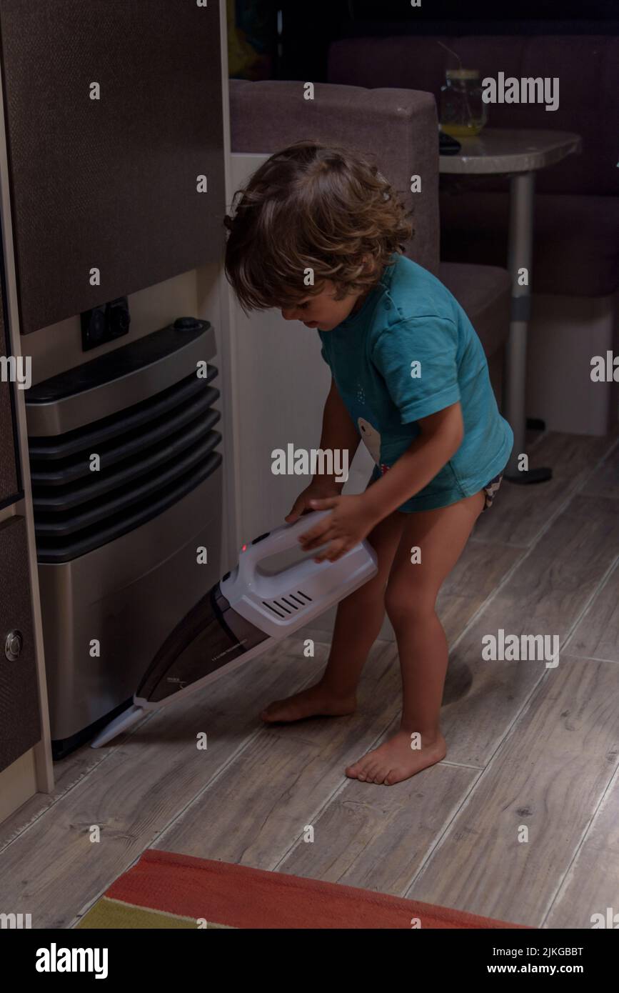 A sweet little boy vacuums the caravan while on vacation. A cute boy is ...