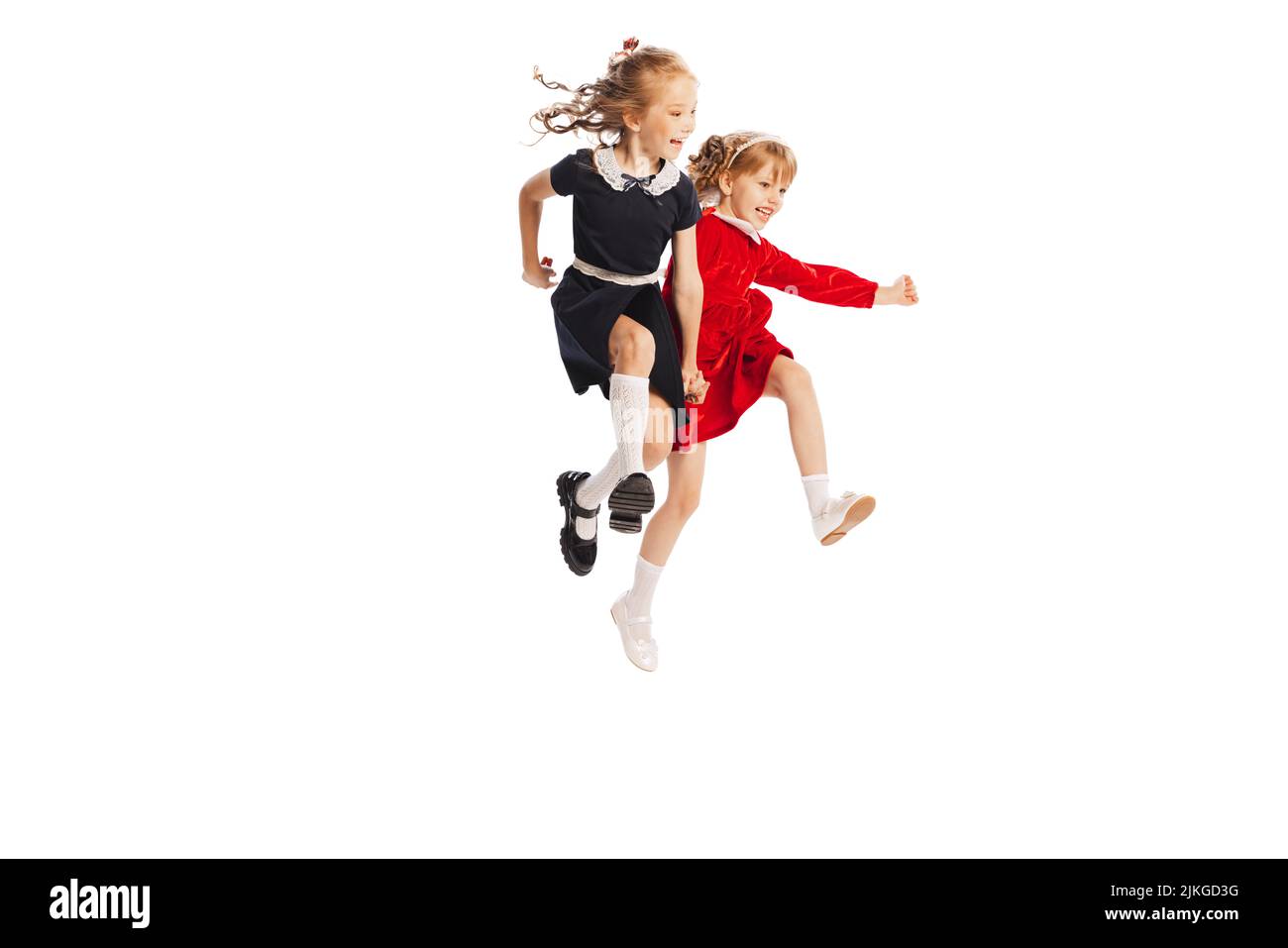 Portrait of two cheerful girls, children jumping over puddle, running ...
