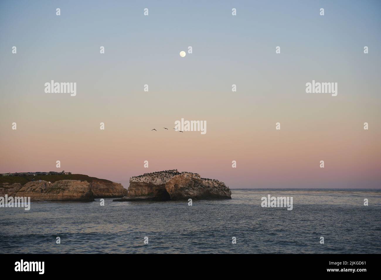 A scenic view of birds flying in the sunset sky above rocky cliffs ...