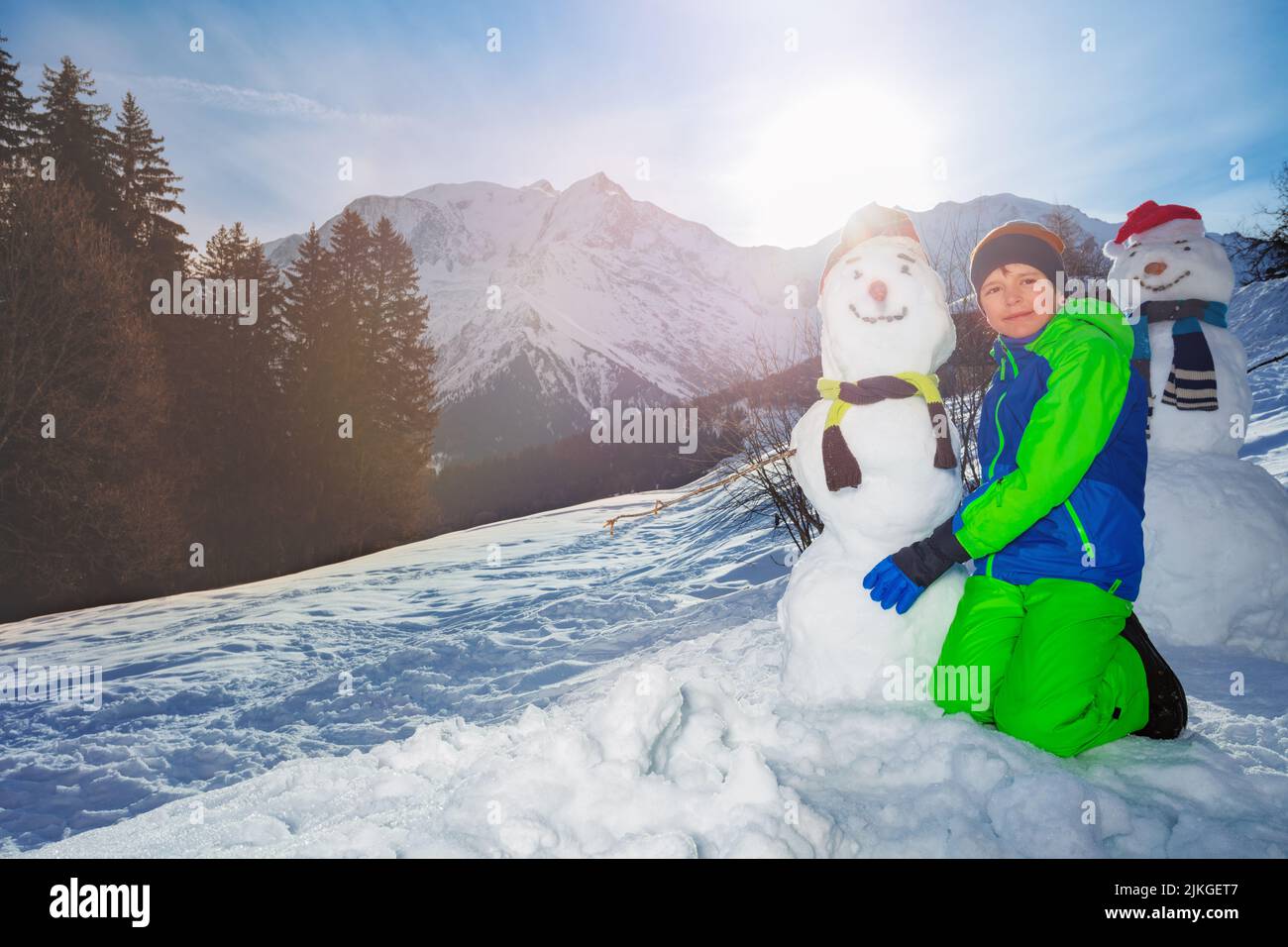 Boy build snowman dress with scarf, hat outside over mountains Stock ...