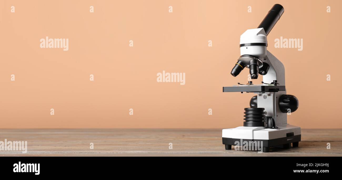 Modern microscope on table against color background with space for text ...
