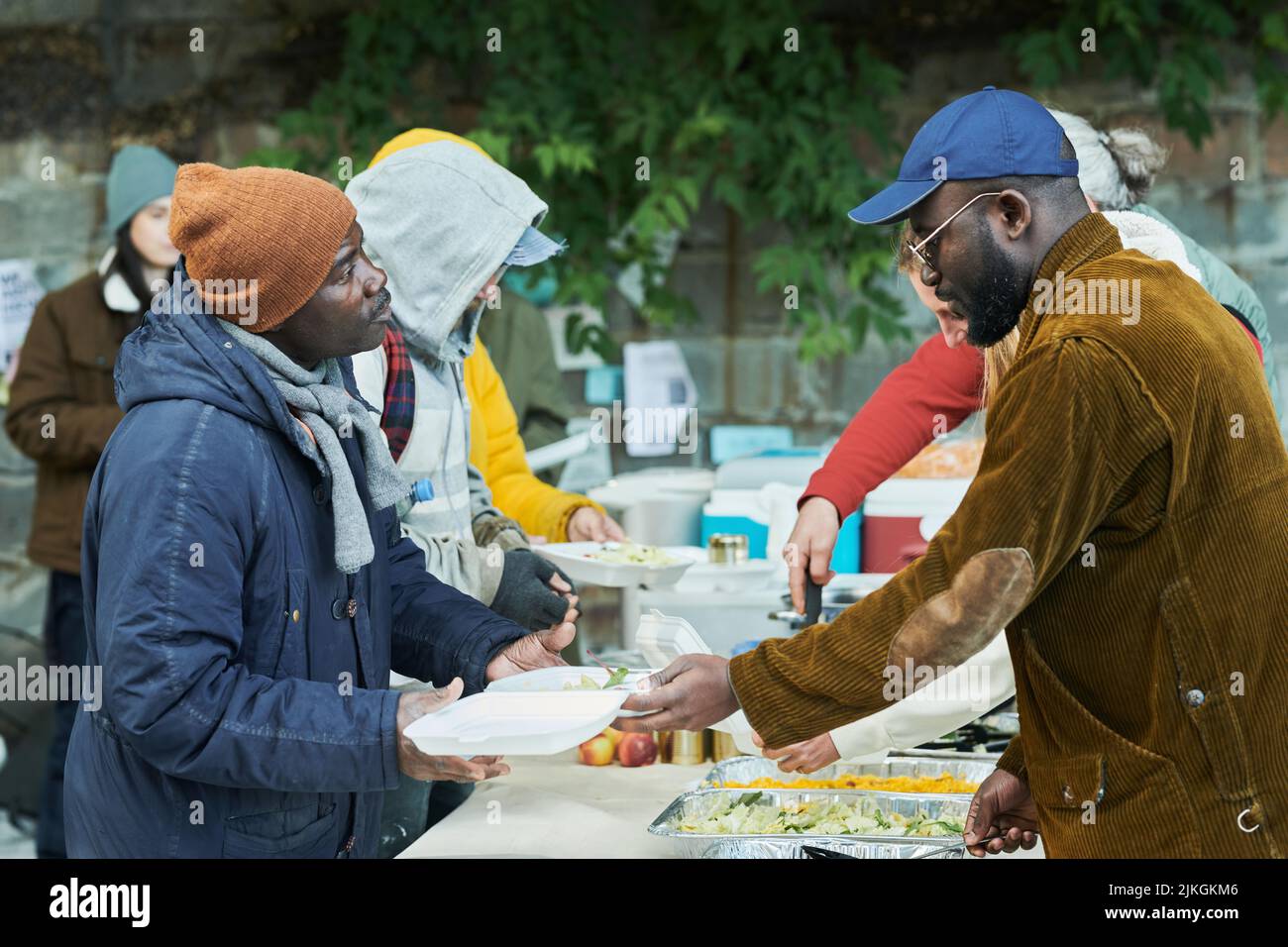 Volunteers sharing food to the poor people outdoors, they putting hot ...