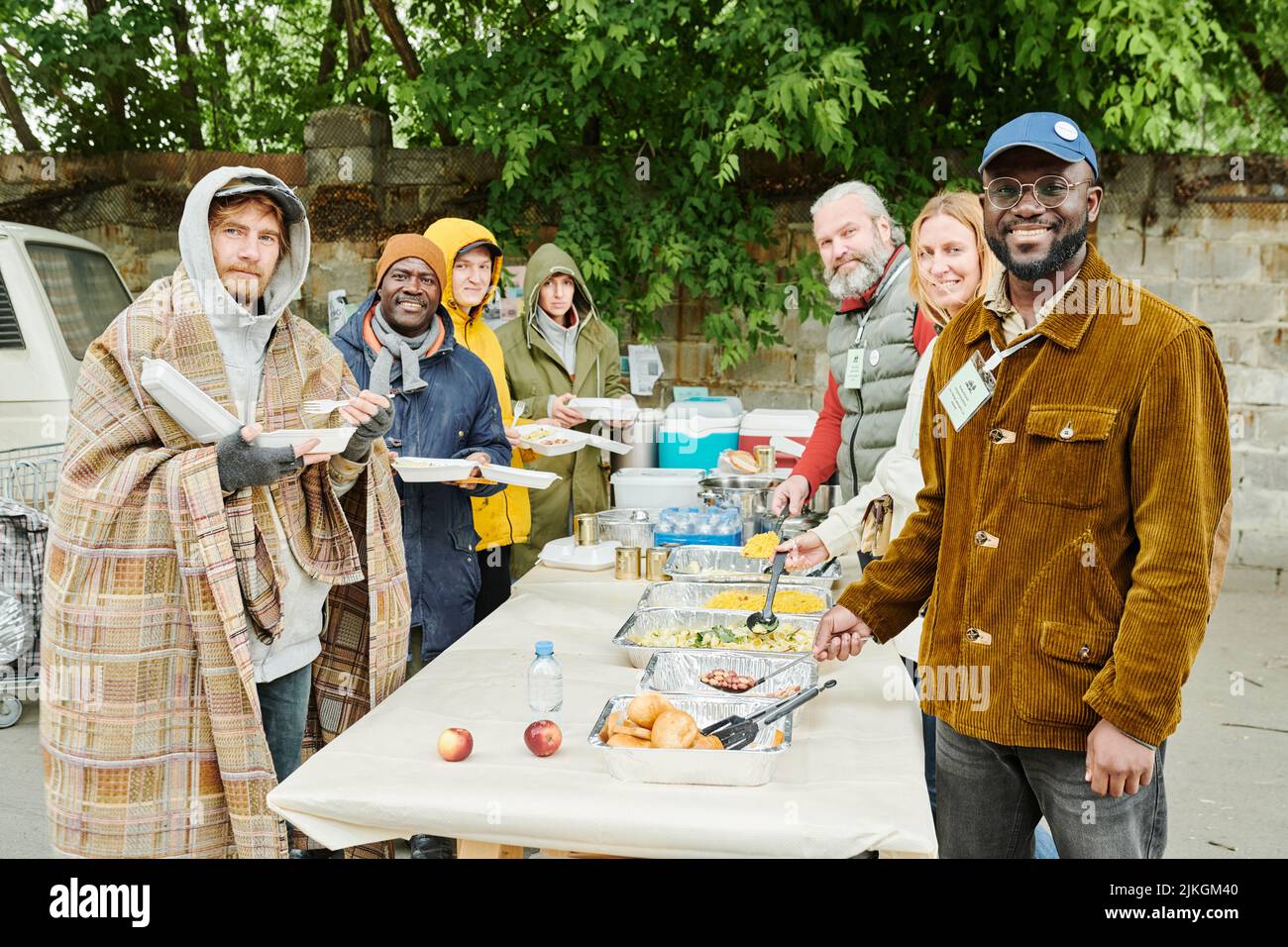 Portrait of group of volunteers and homeless people smiling at camera ...