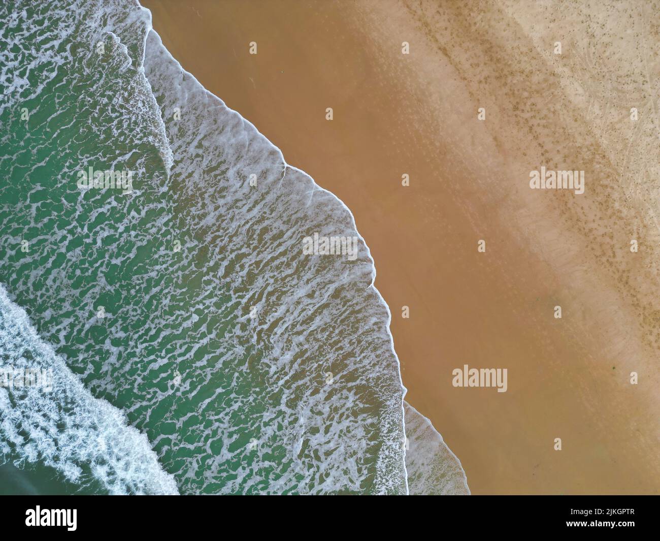 An aerial drone view of foamy waves rolling and crashing on sandy ...