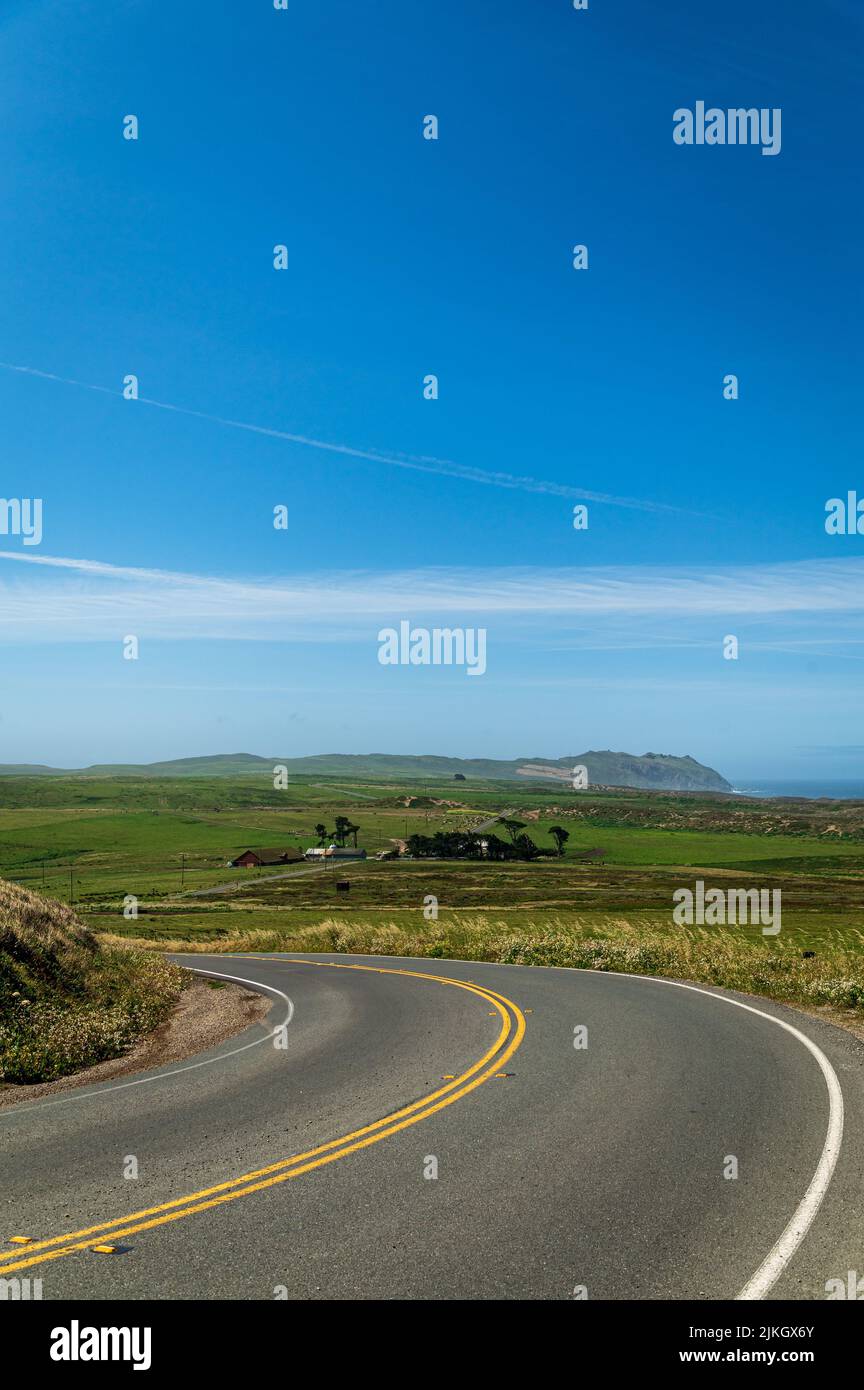 A vertical shot of a two-way asphalt road passing through green fields ...