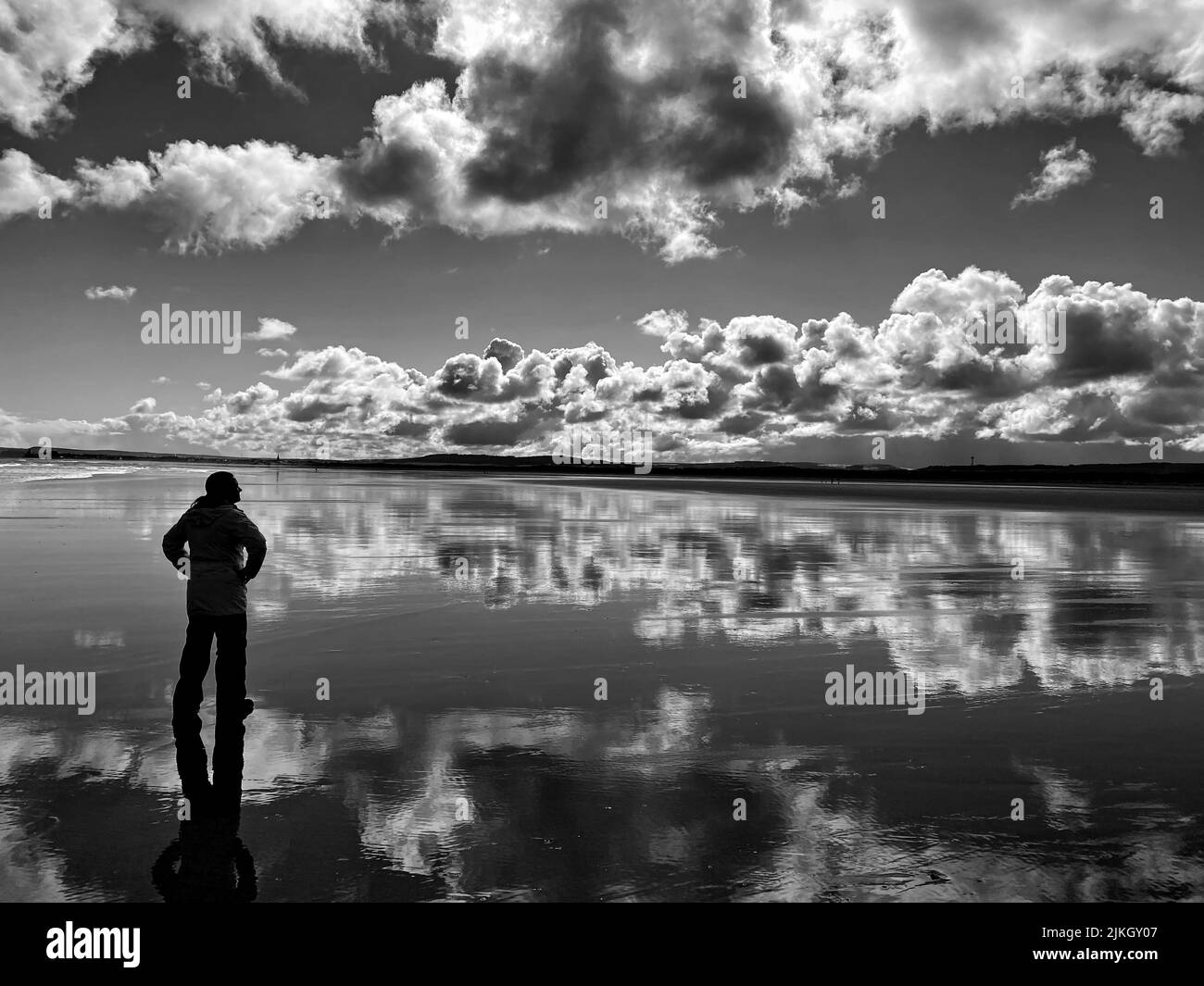 A grayscale shot of a person silhouette standing on a lake shore with ...
