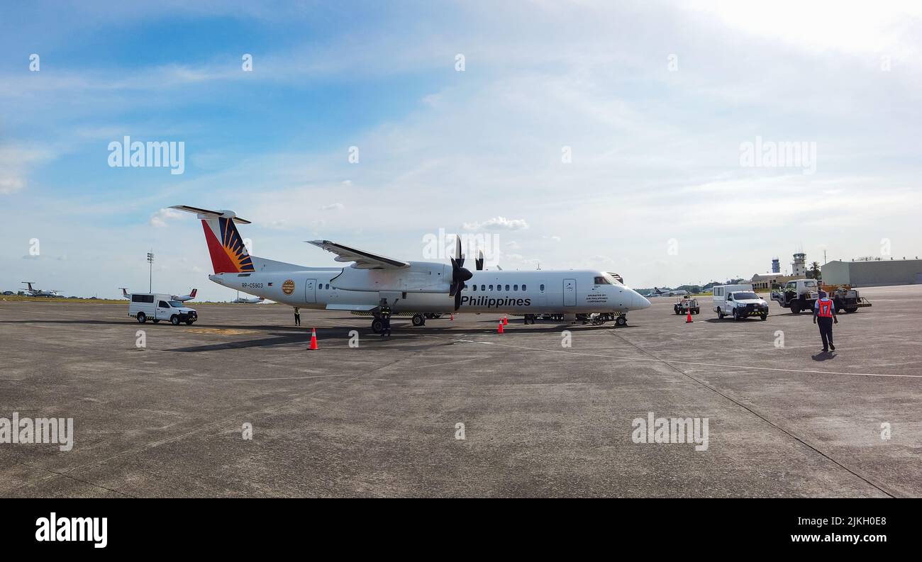 A medium-sized plane parked on the tarmac under a bright cloudy sky ...