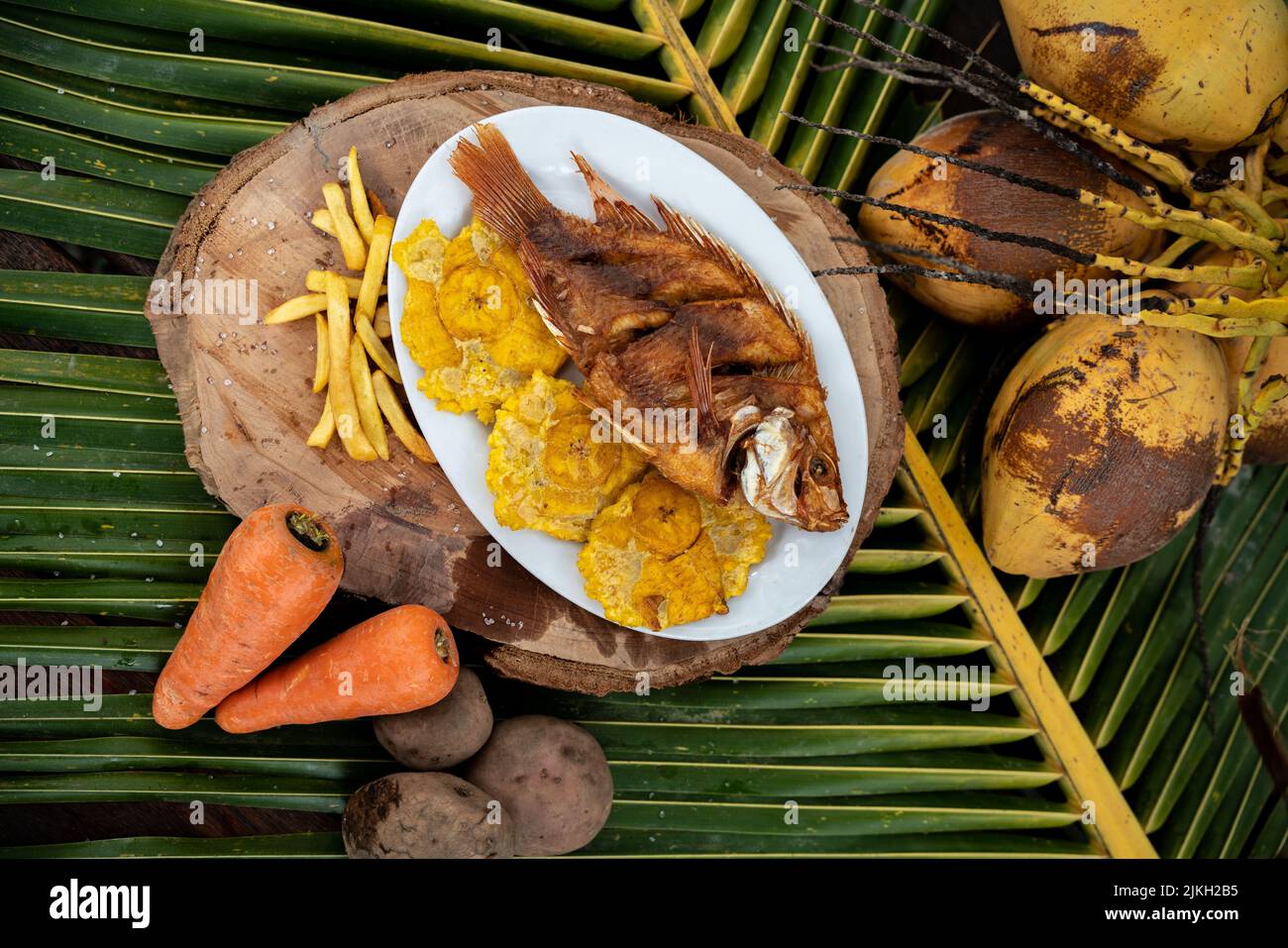 A top view of a cooked fish and fried plantains on a log board on a ...