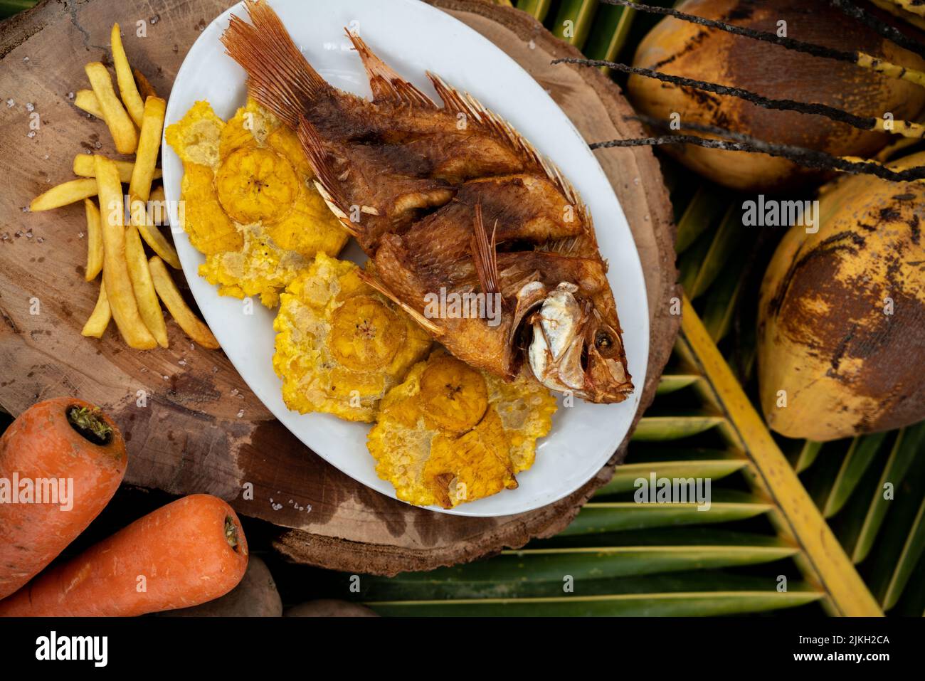 A top view of a cooked whole fish and fried plantains on a plate on a ...