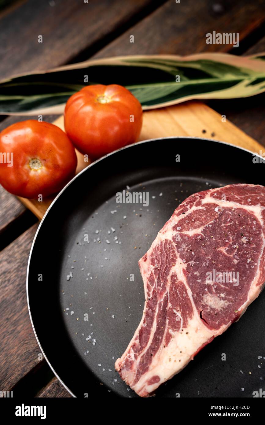 A vertical shot of a slice of raw red steak on a black pan on a board ...