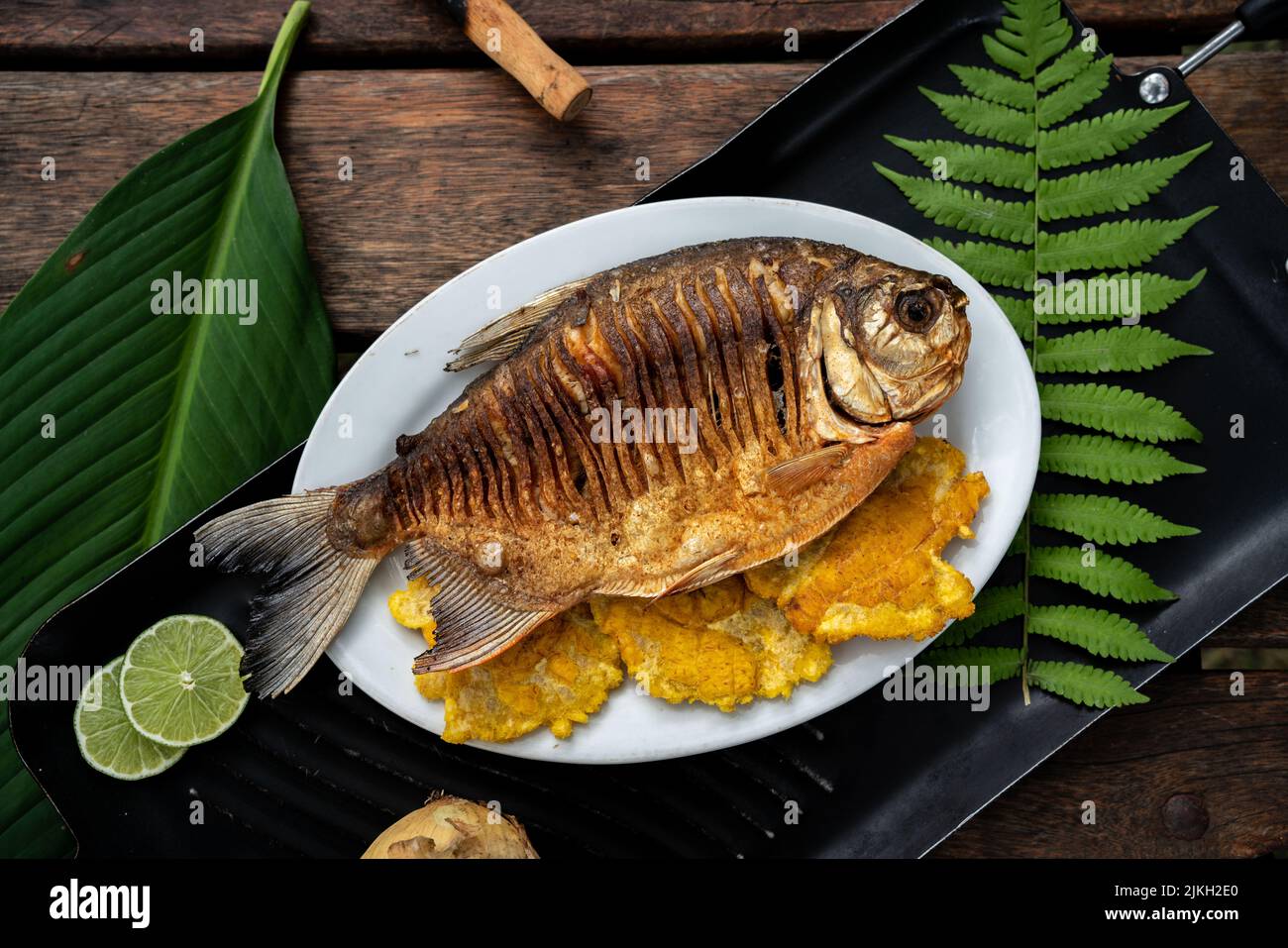 A top view of a cooked whole fish and fried plantains on a plate on a ...