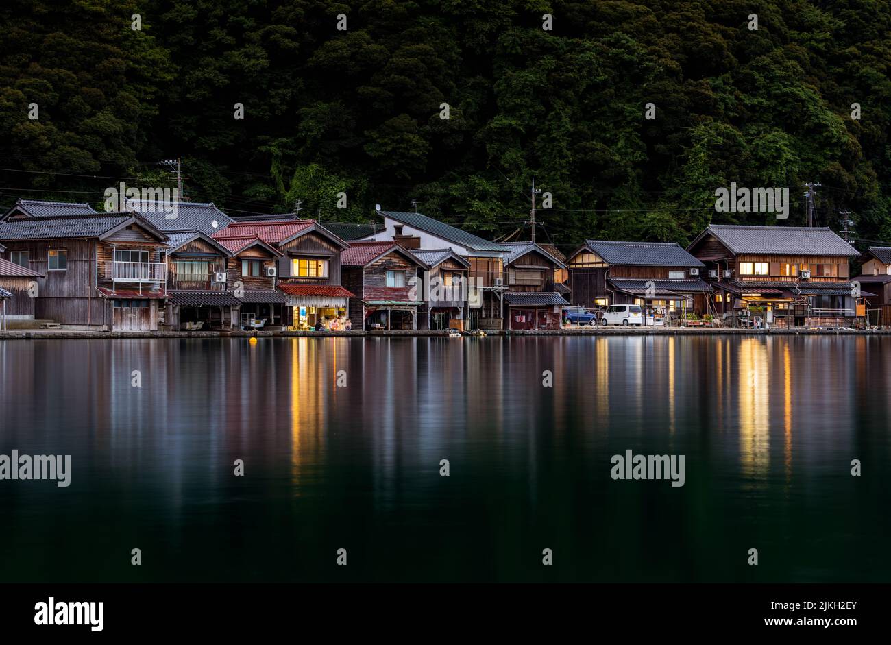 Traditional wooden boathouses reflect of calm water as night falls on ...