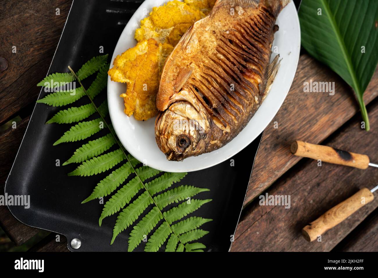 A top view of a whole cooked fish and fried plantains on a plate on a ...