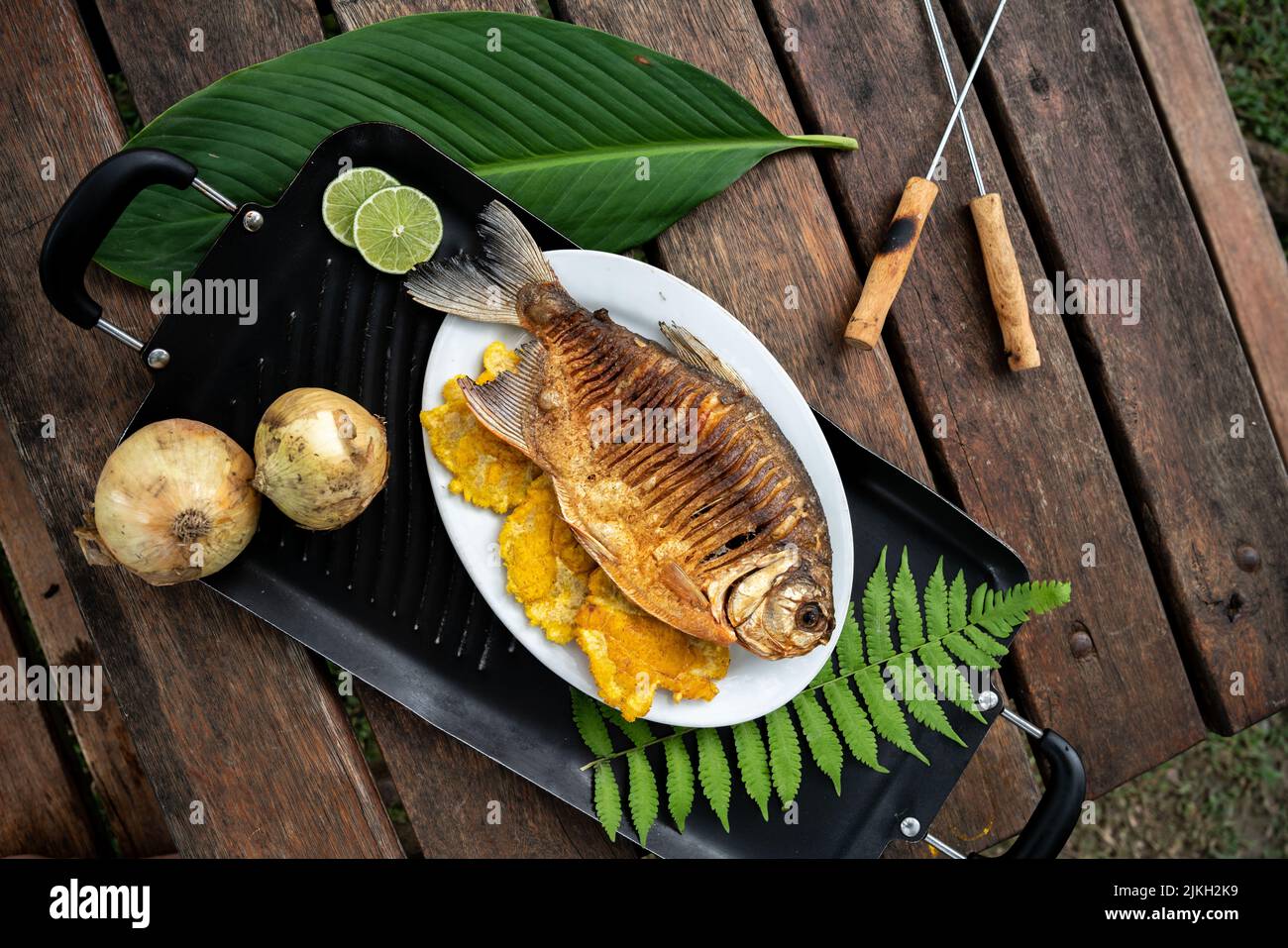 A top view of a plate of cooked fish and fried plantains on a black ...