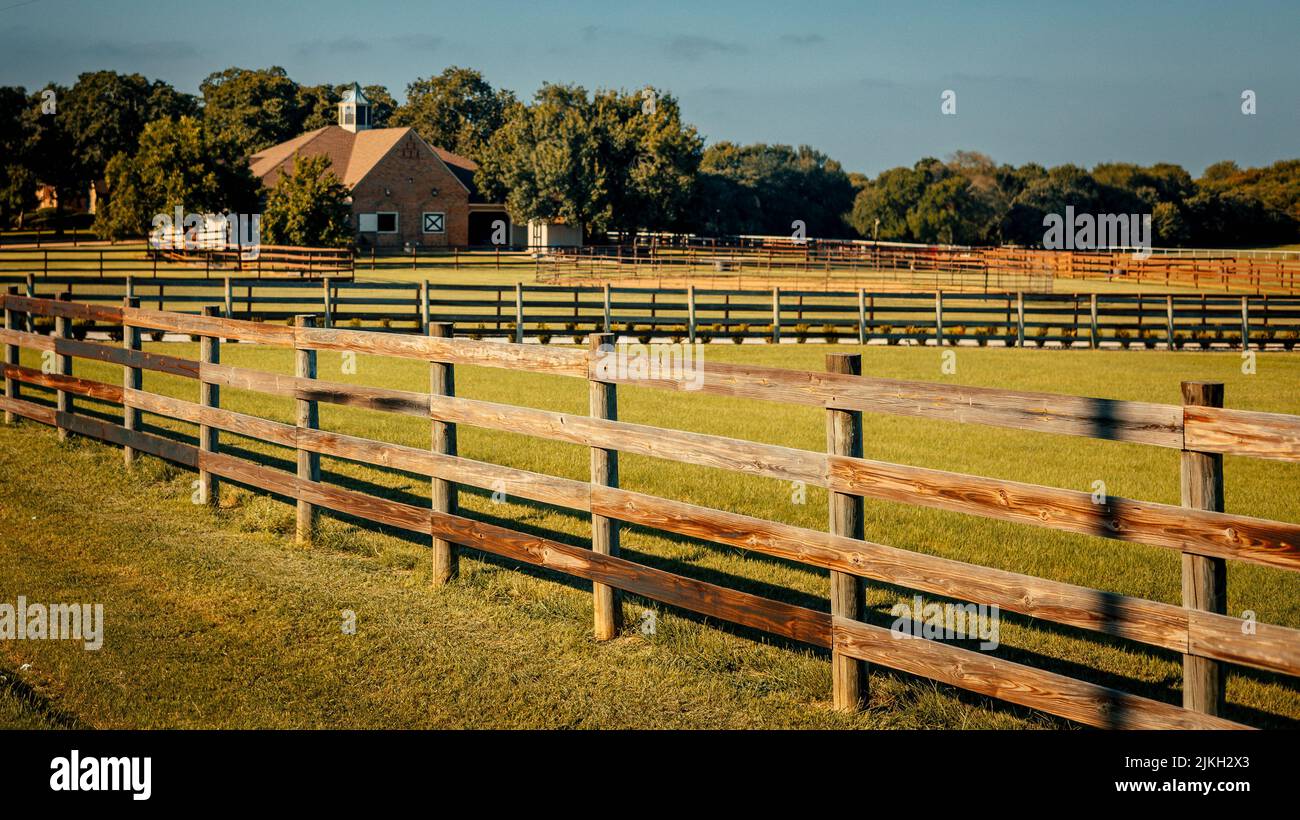 A scenic view of pasture surrounded by a wooden fence against a farm on ...