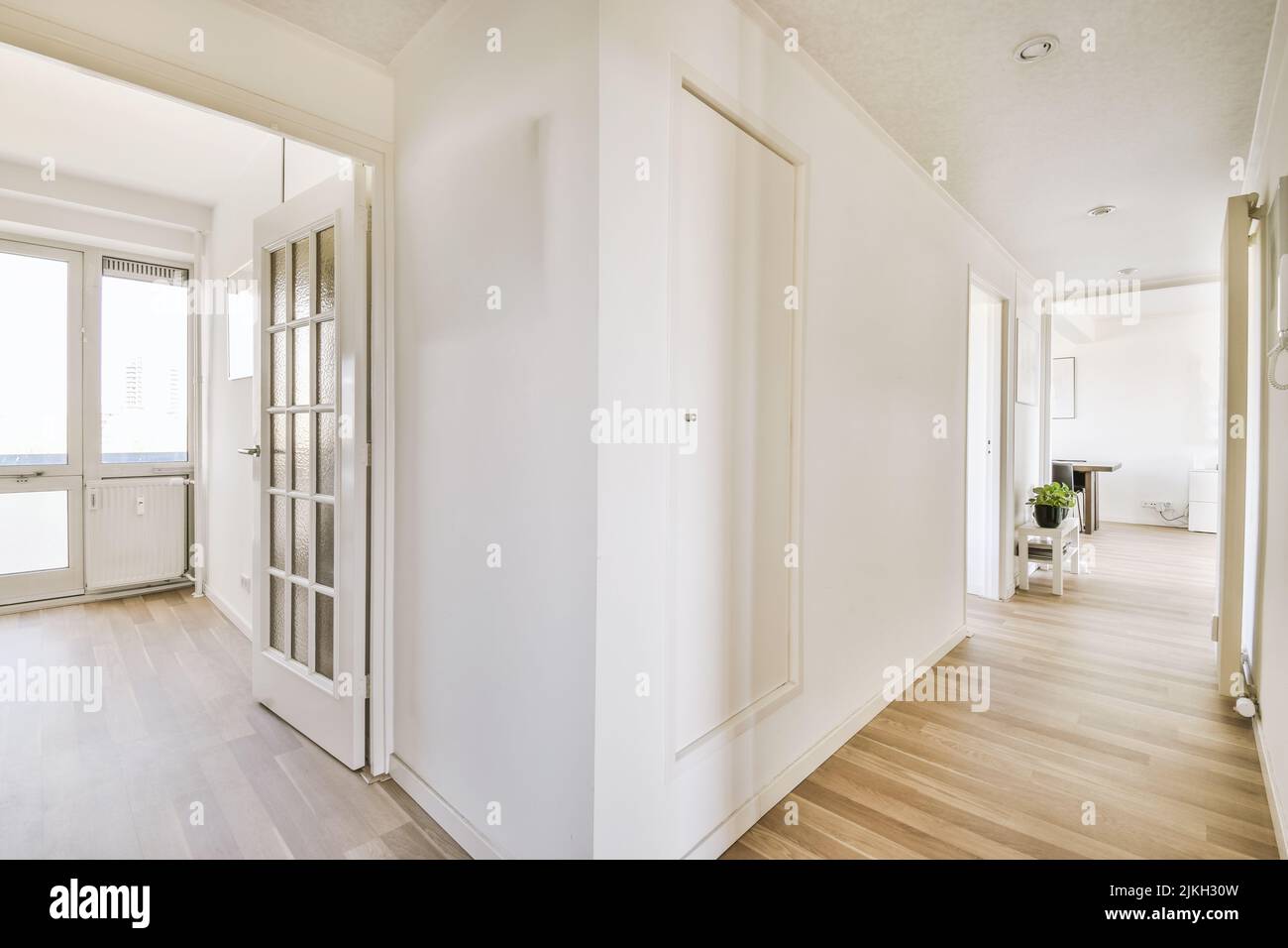 Narrow corridor with white walls and doors leading to spacious room ...