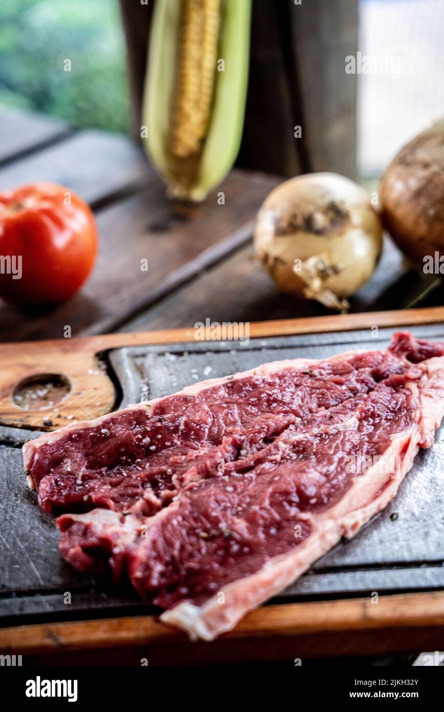 A vertical shot of a seasoned raw red steak slice on a cooking board ...