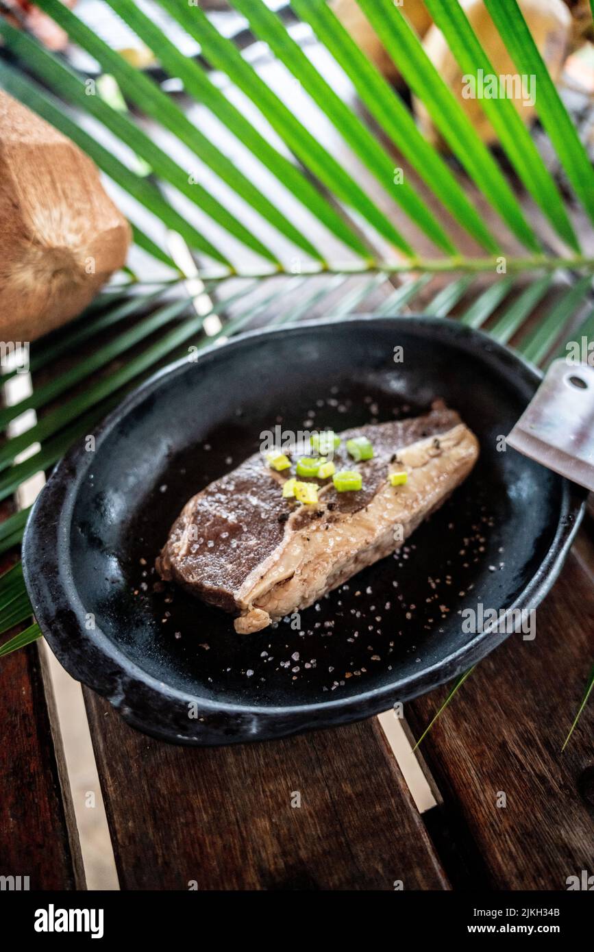 A vertical shot of a steak cooking in a black pan with spring onion ...