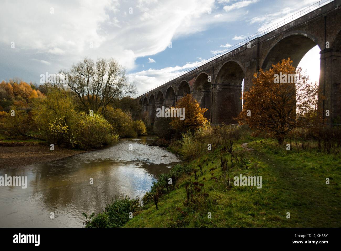 A high arched stone bridge over a river with autumn trees in a park ...