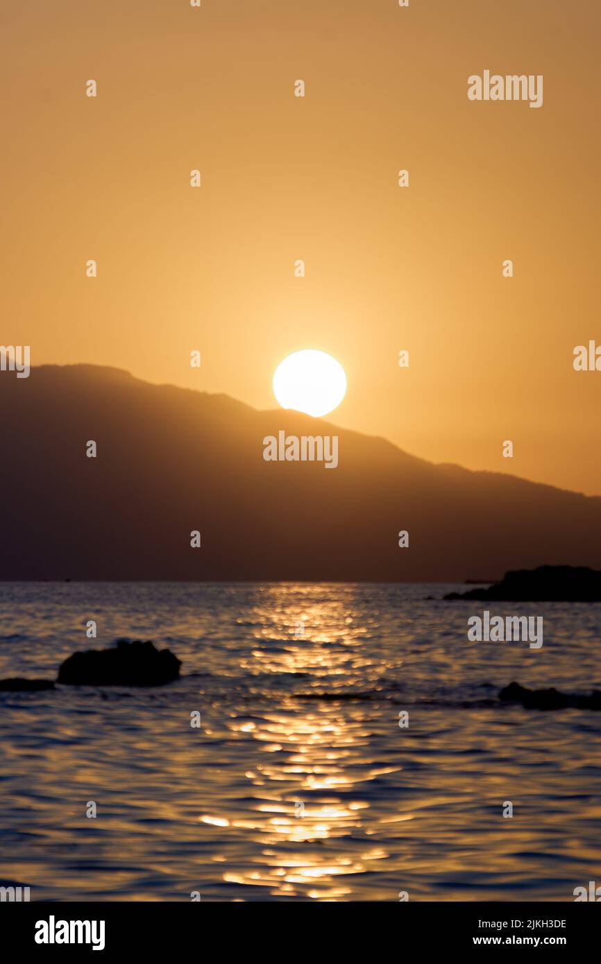 A vertical shot of the sea and sun sinking behind the hill Stock Photo ... A vertical shot of the sea and sun sinking behind the hill Stock Photo ...