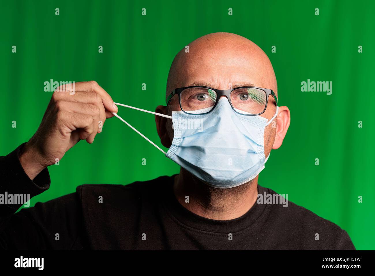 portrait bald man with glasses and green background with covid mask ...