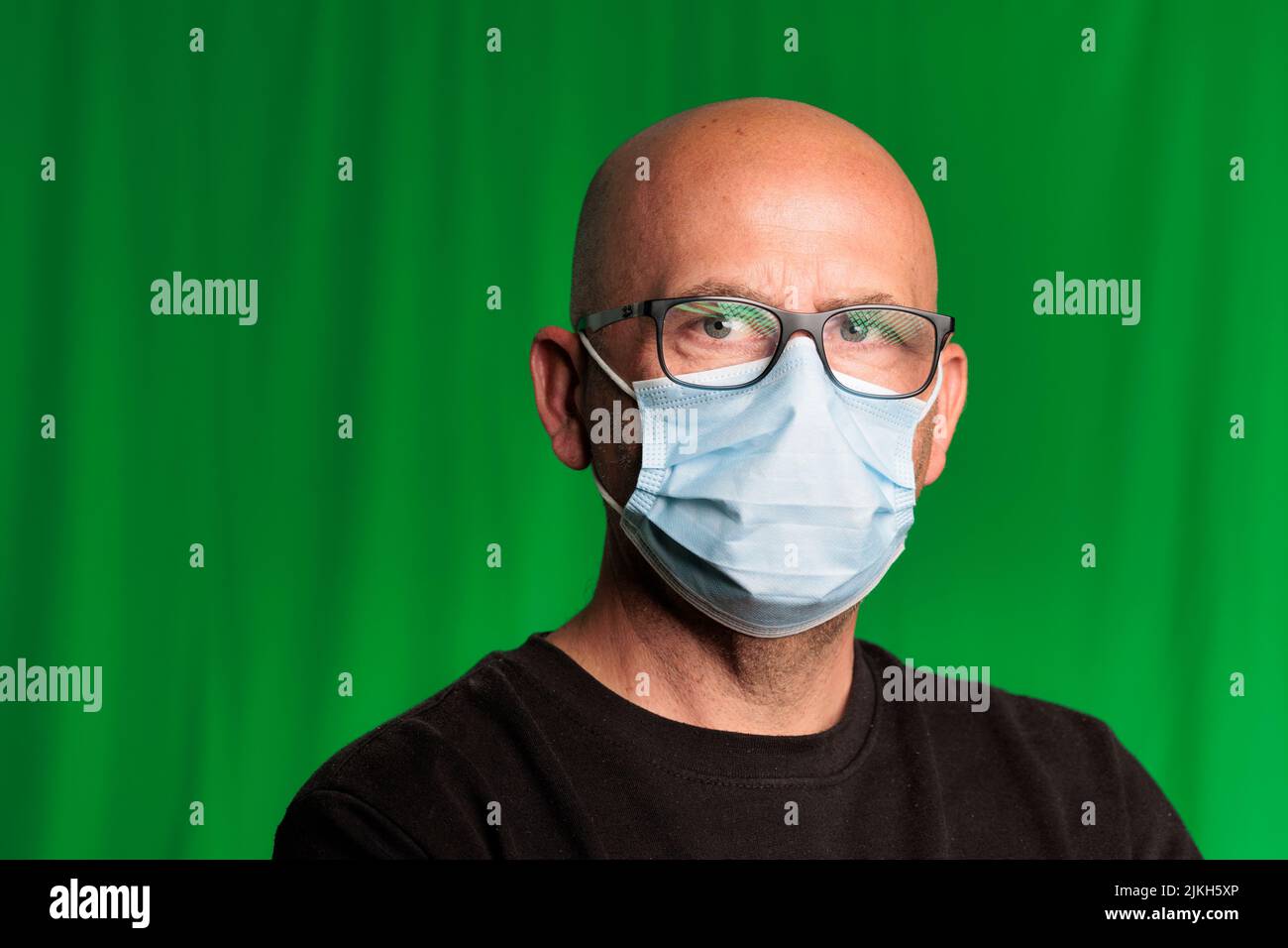 portrait bald man with glasses and green background with covid mask ...